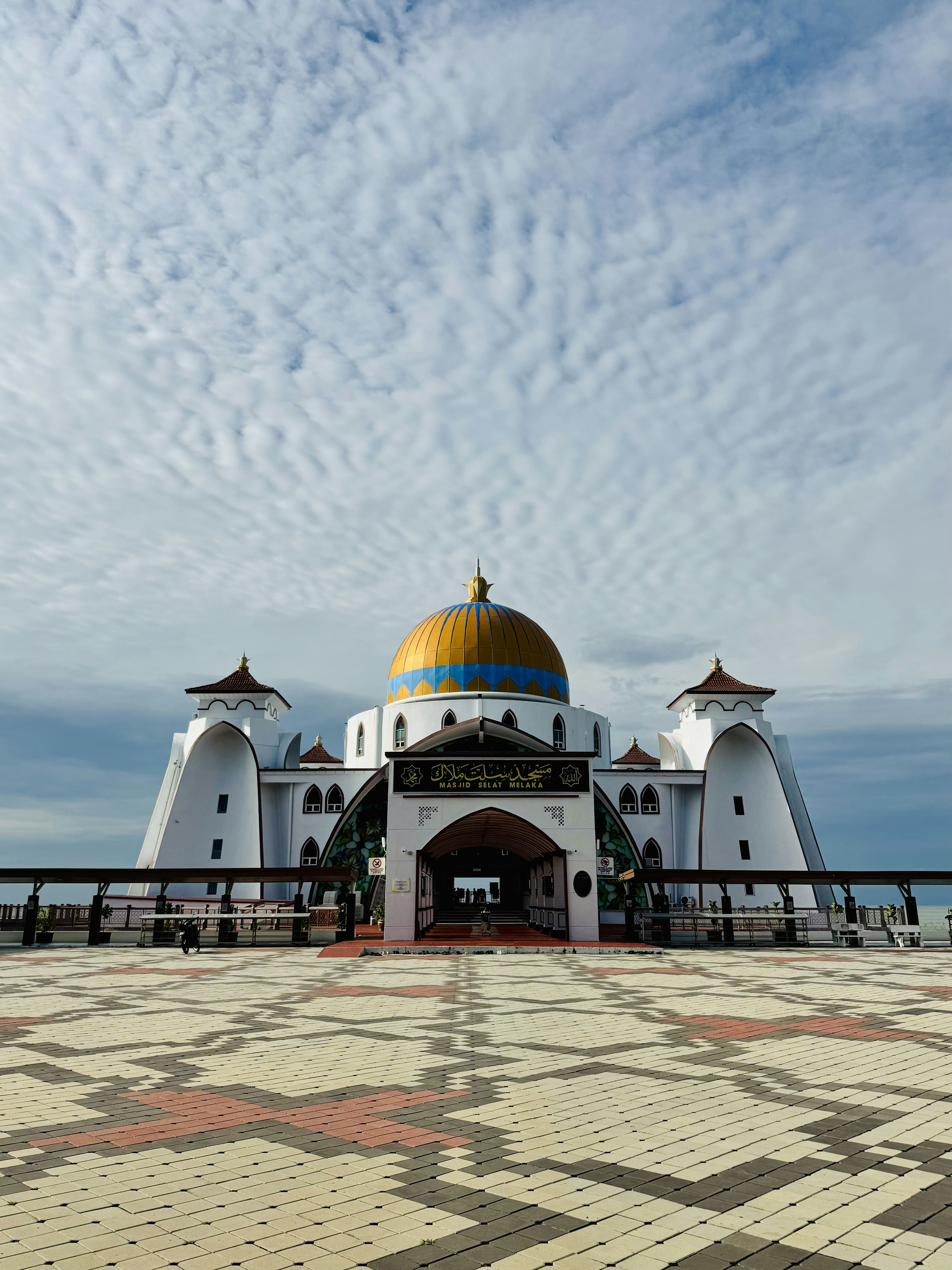 White mosque with a golden dome under a cloudy sky.