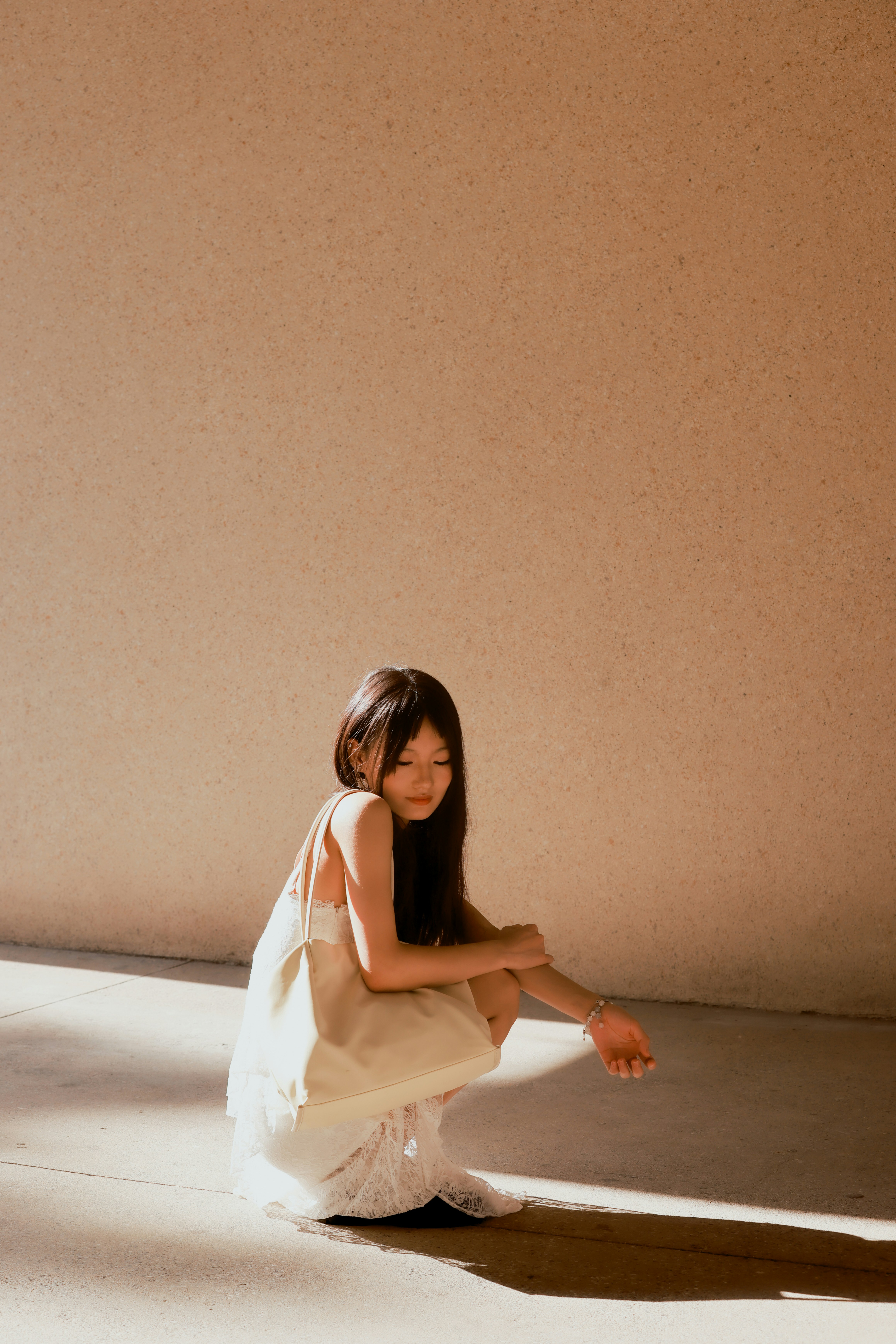 Quiet Solitude in Sunlit Corner: A Young woman in white sits against a warm stucco backdrop