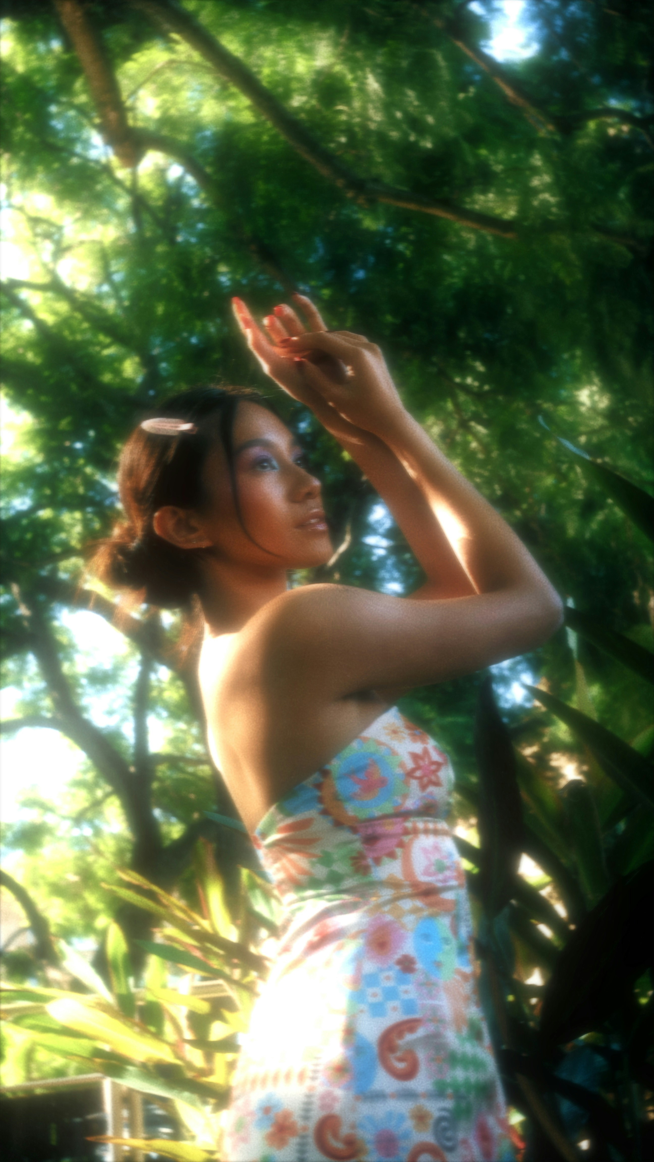 Young woman in a vibrant dress under sunlit green trees.
