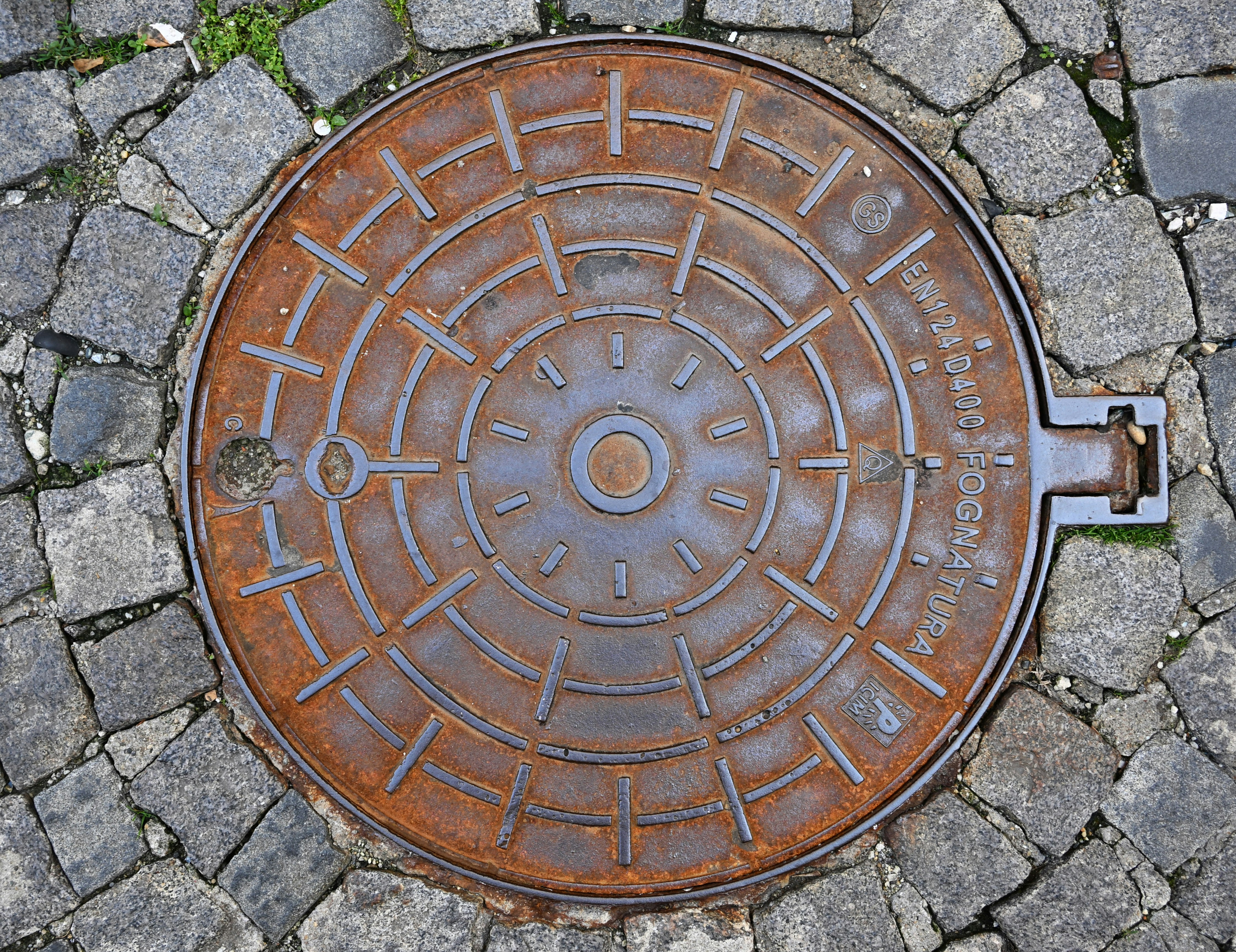 Circular Atlas: Weathered Manhole Amid Cobblestones