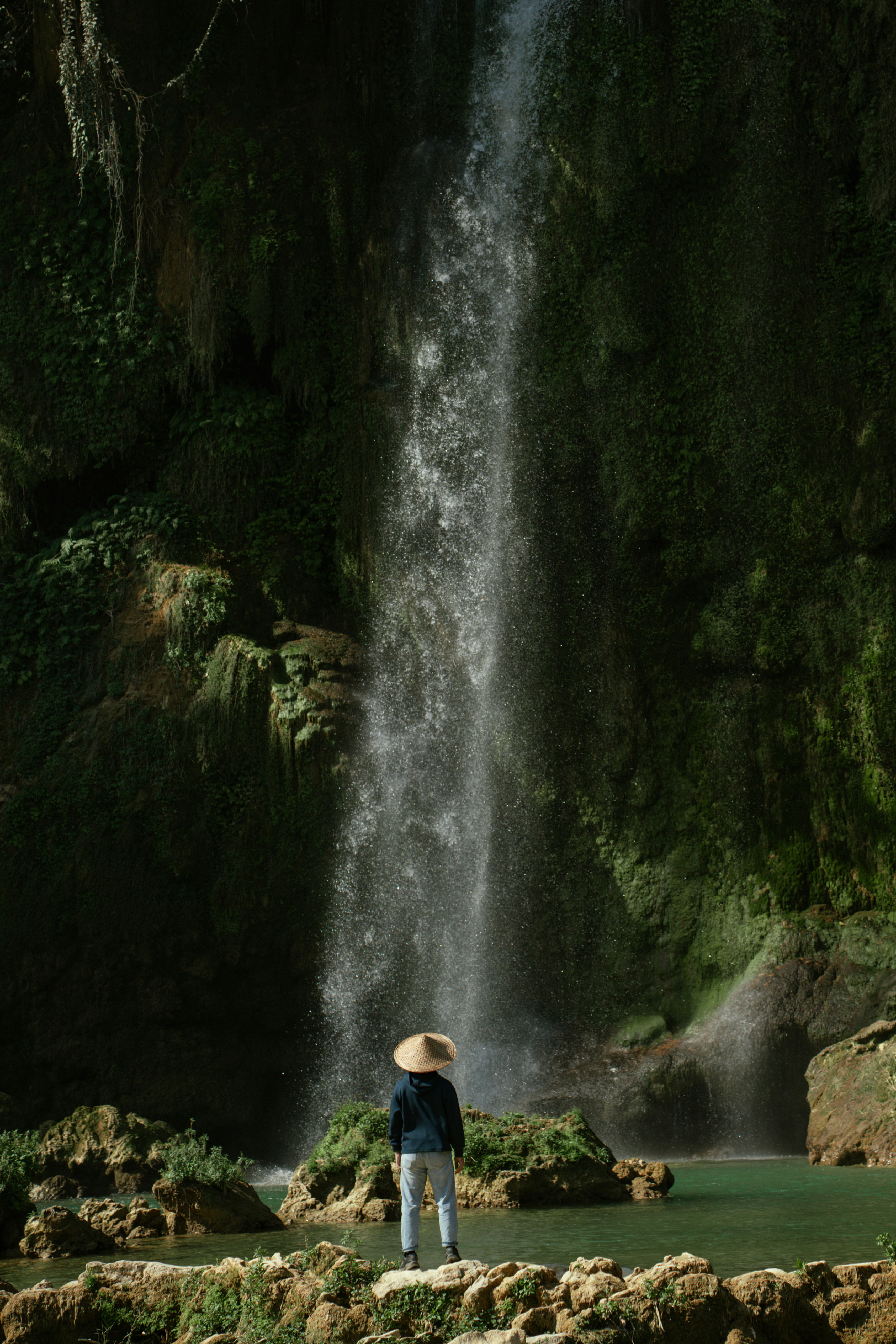 Liquid Veil: A lone figure at the base of a moss-green waterfall