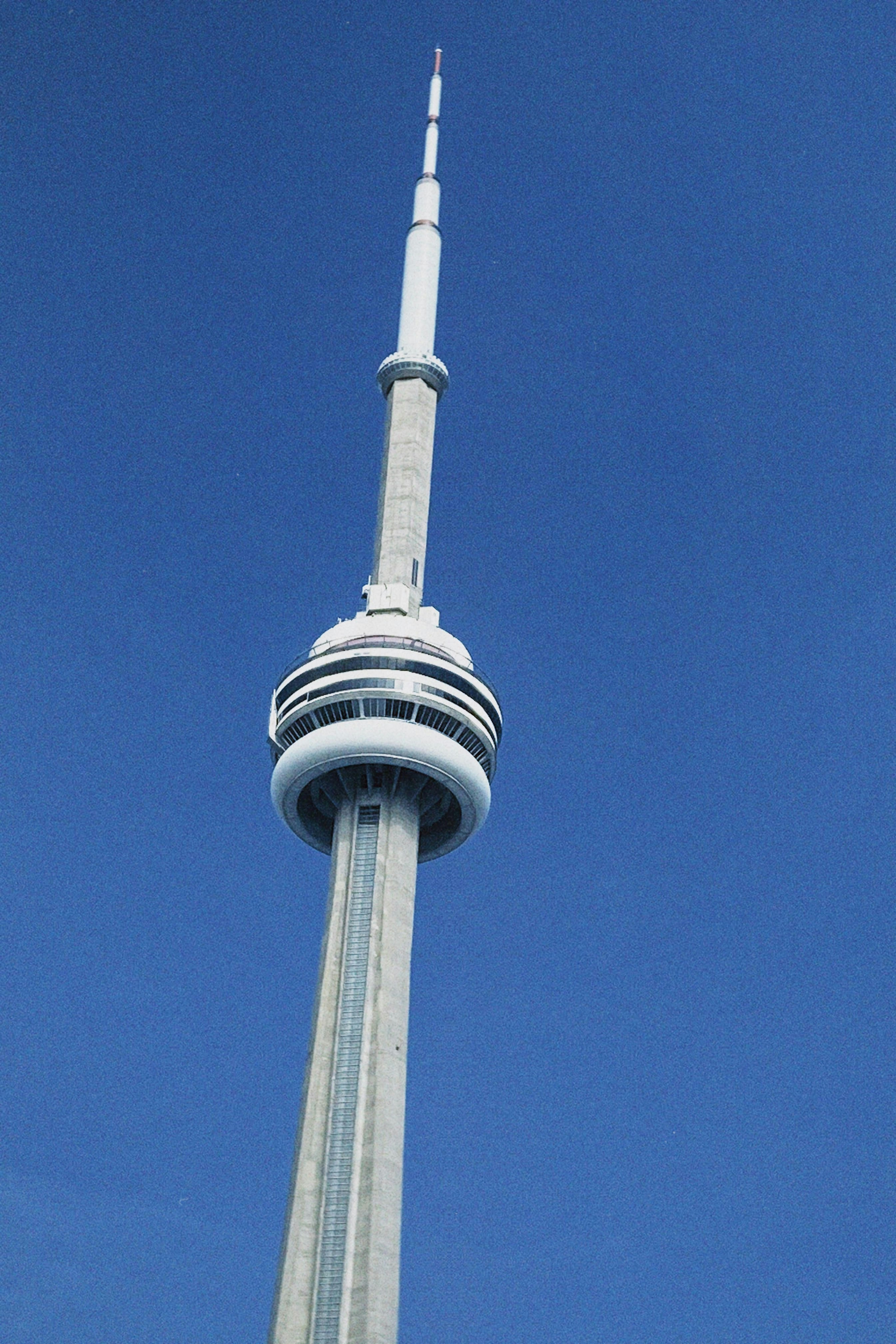 Captured from a low-angle perspective, this shot emphasizes the sheer vertical scale and brutalist elegance of a global landmark. The composition utilizes a clean diagonal orientation to create dynamic energy, set against a deep, grain-rich sky. The focus remains on the structural details of the main pod and antenna, turning a massive architectural feat into a sharp, minimalist silhouette.