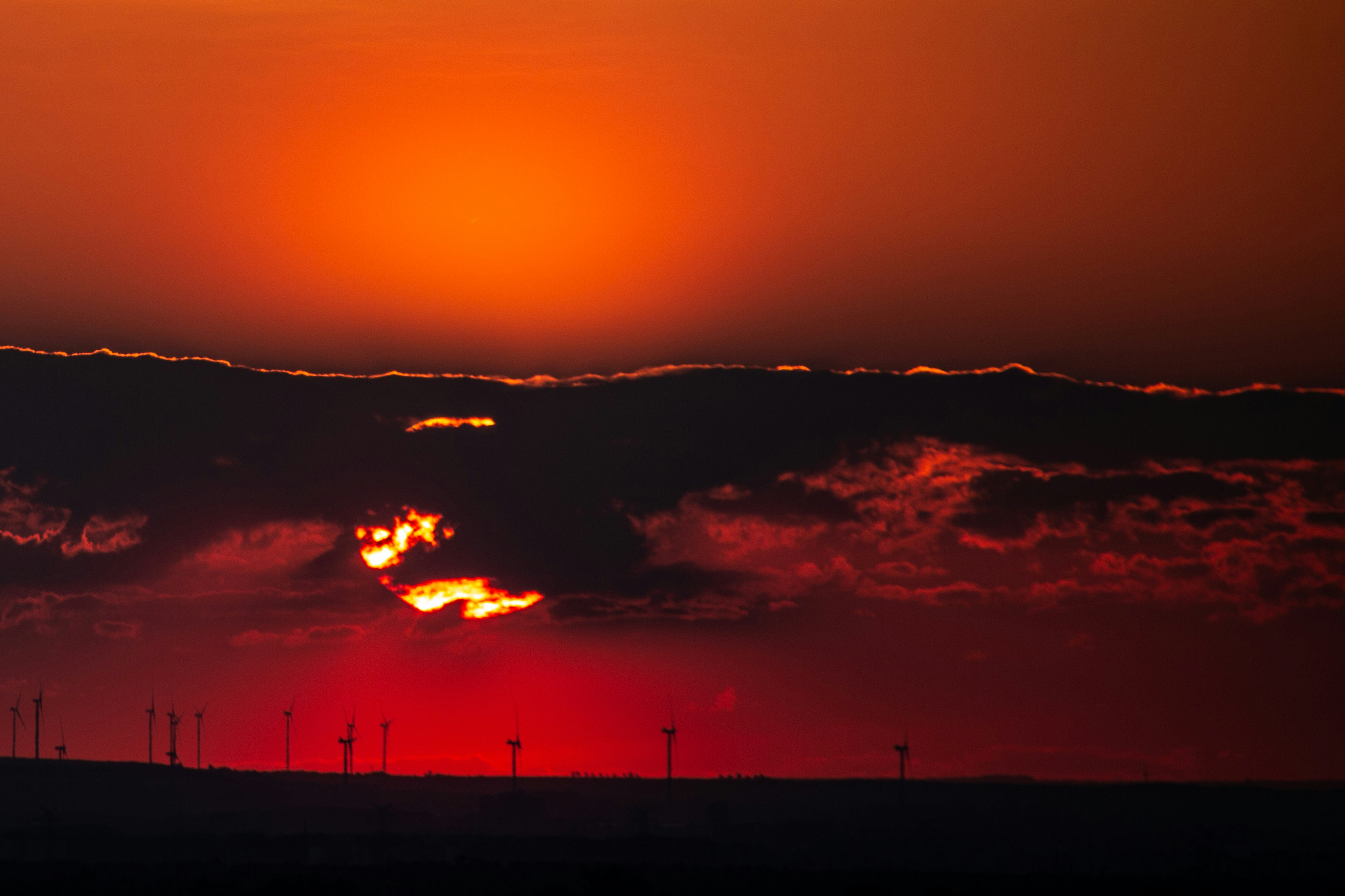 Crimson Horizon: Distant Wind Turbines Silhouetted at Sunset
