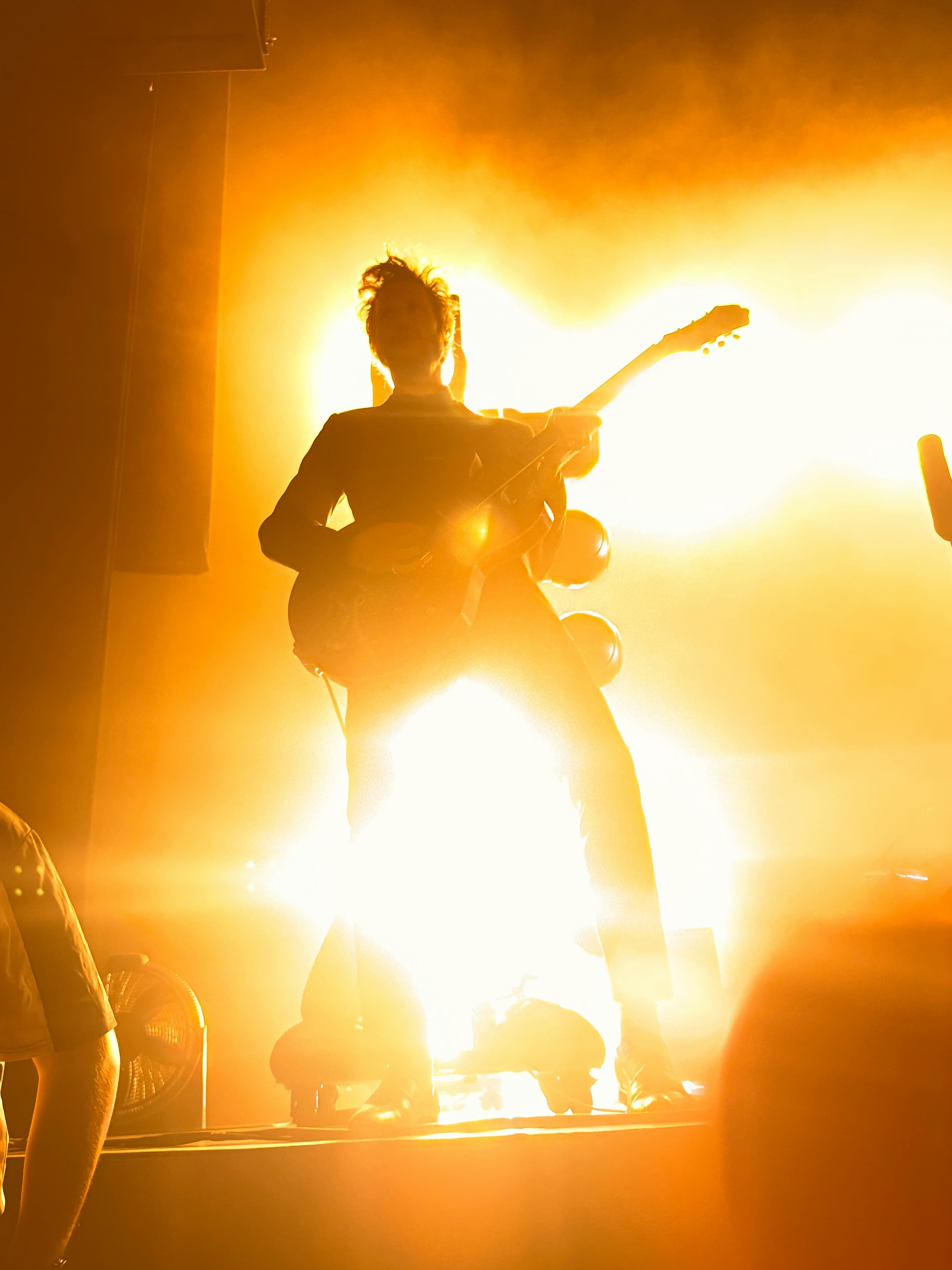 Guitarist bathed in explosive stage light, silhouette against blaze