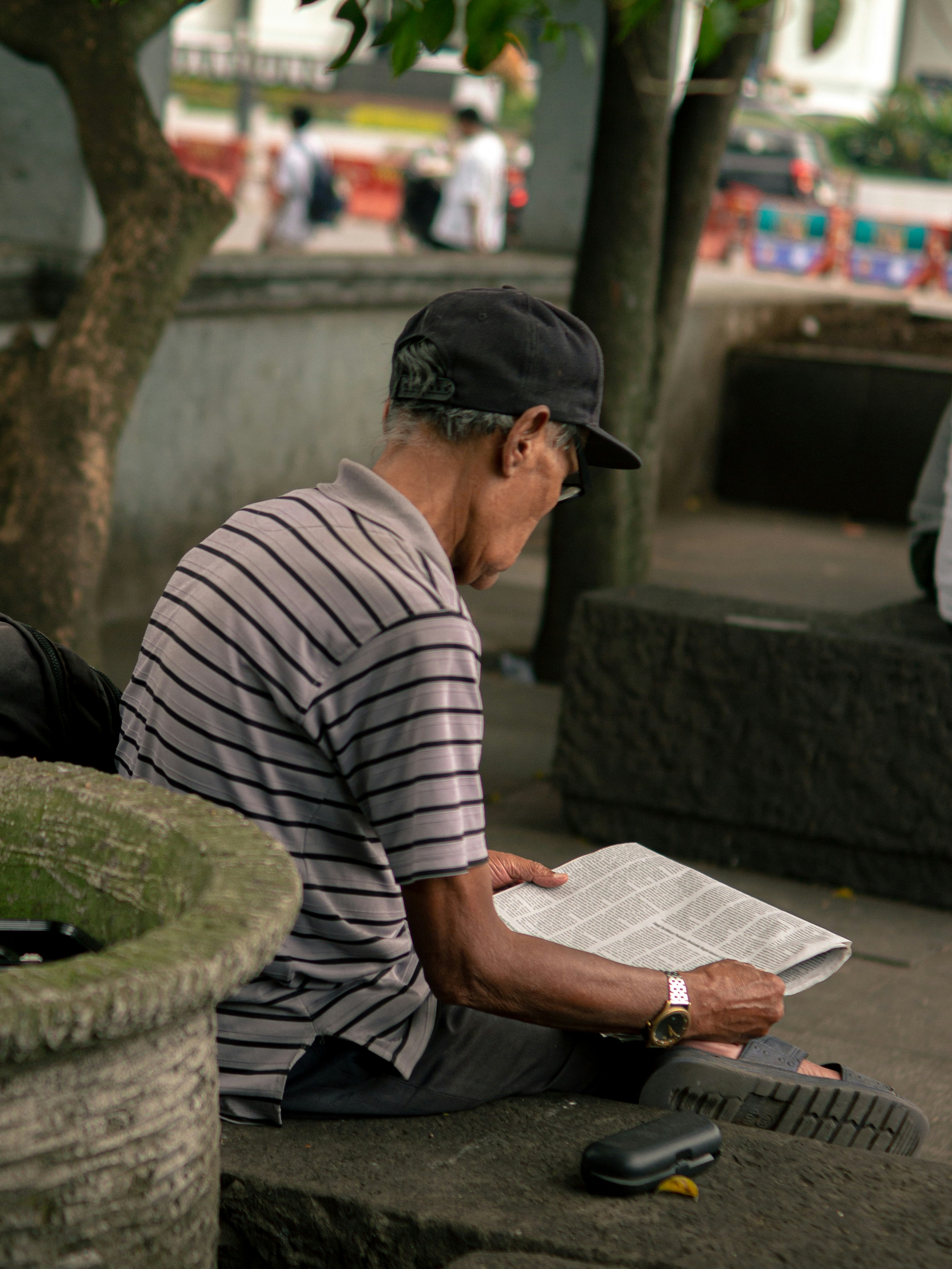 Man in striped shirt reads from a newspaper on a stone bench