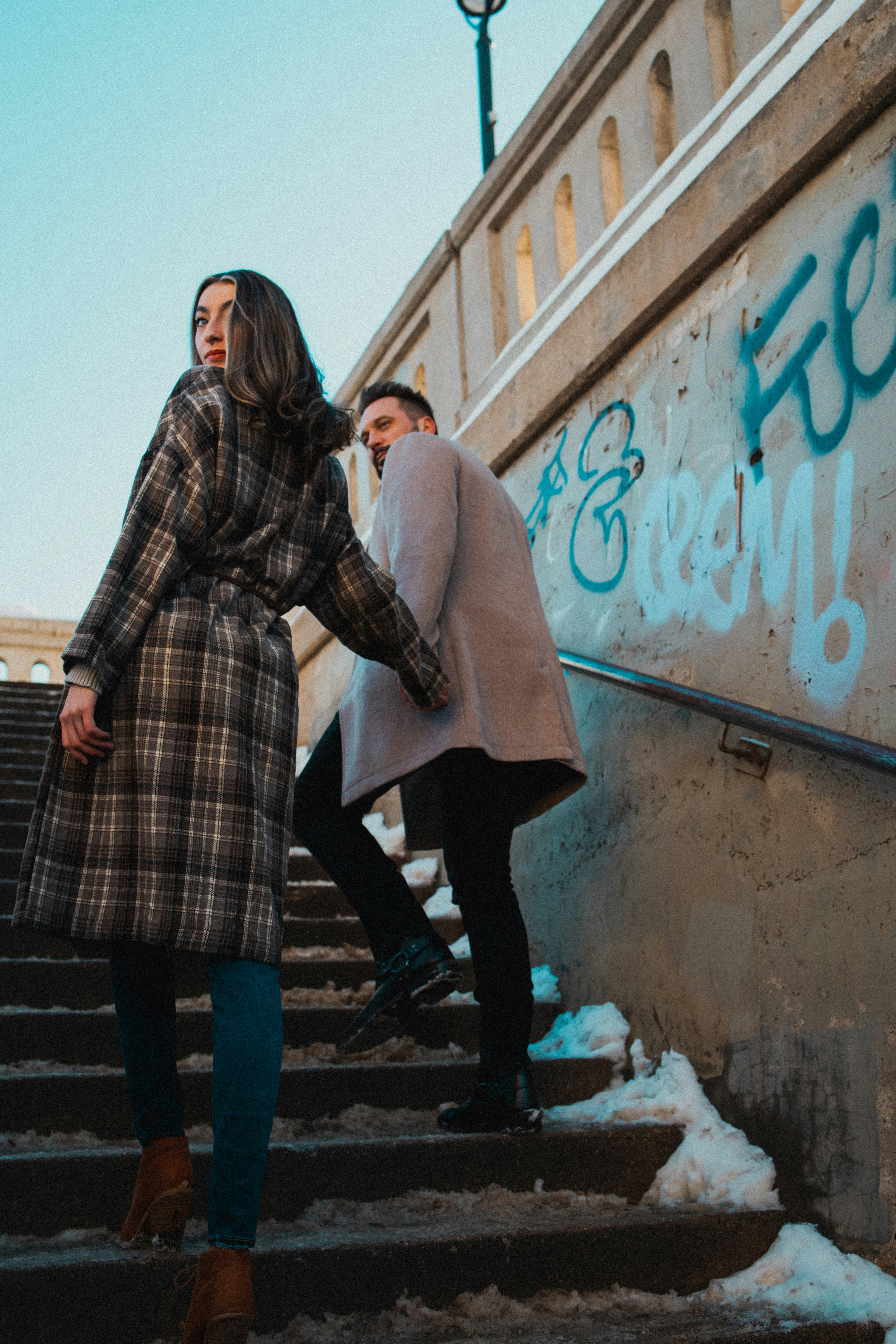Two Figures Ascend a Graffitied Staircase into Cold Light