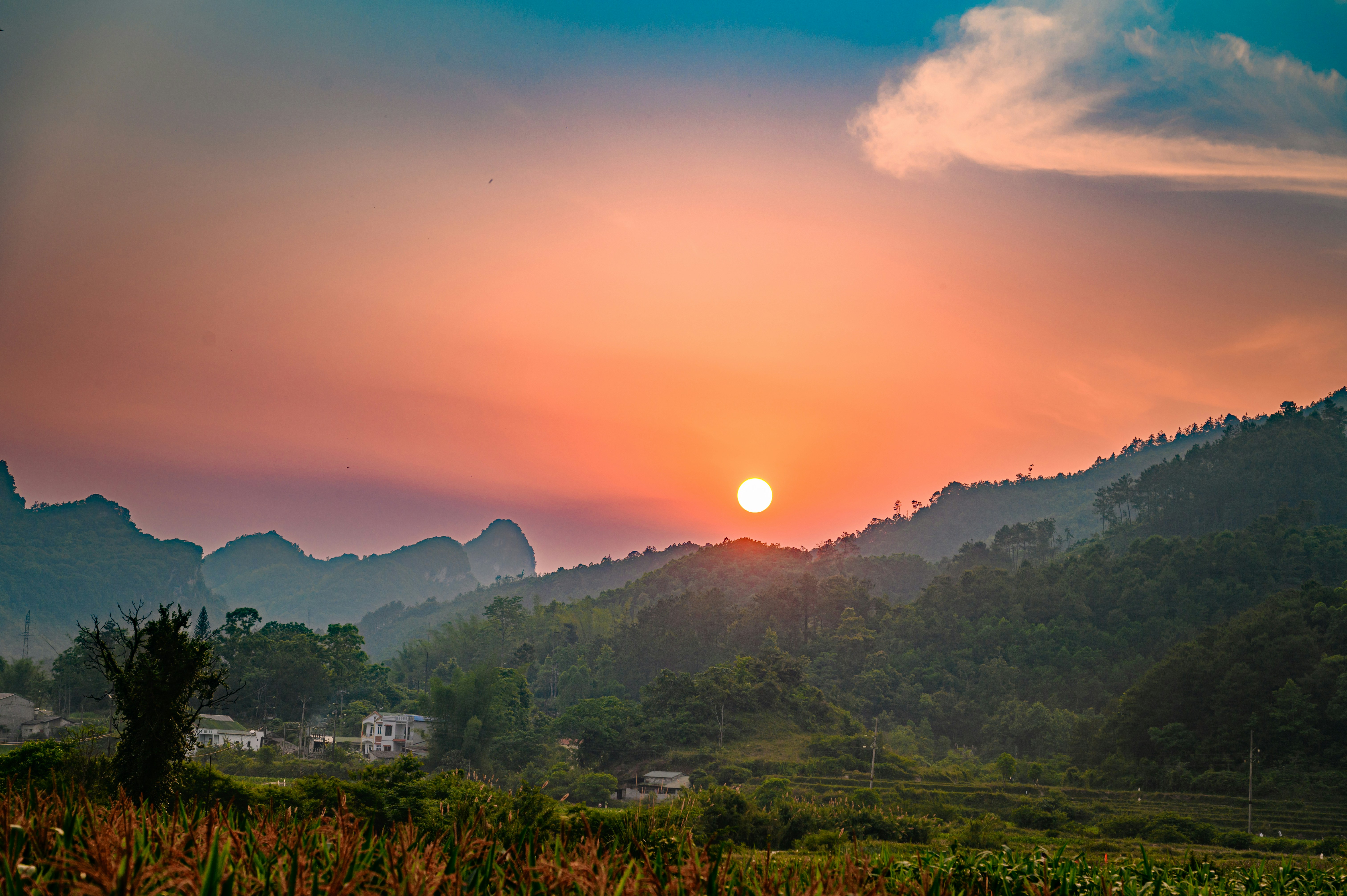 Sunrise over hillside village: warm glow on fields and distant peaks