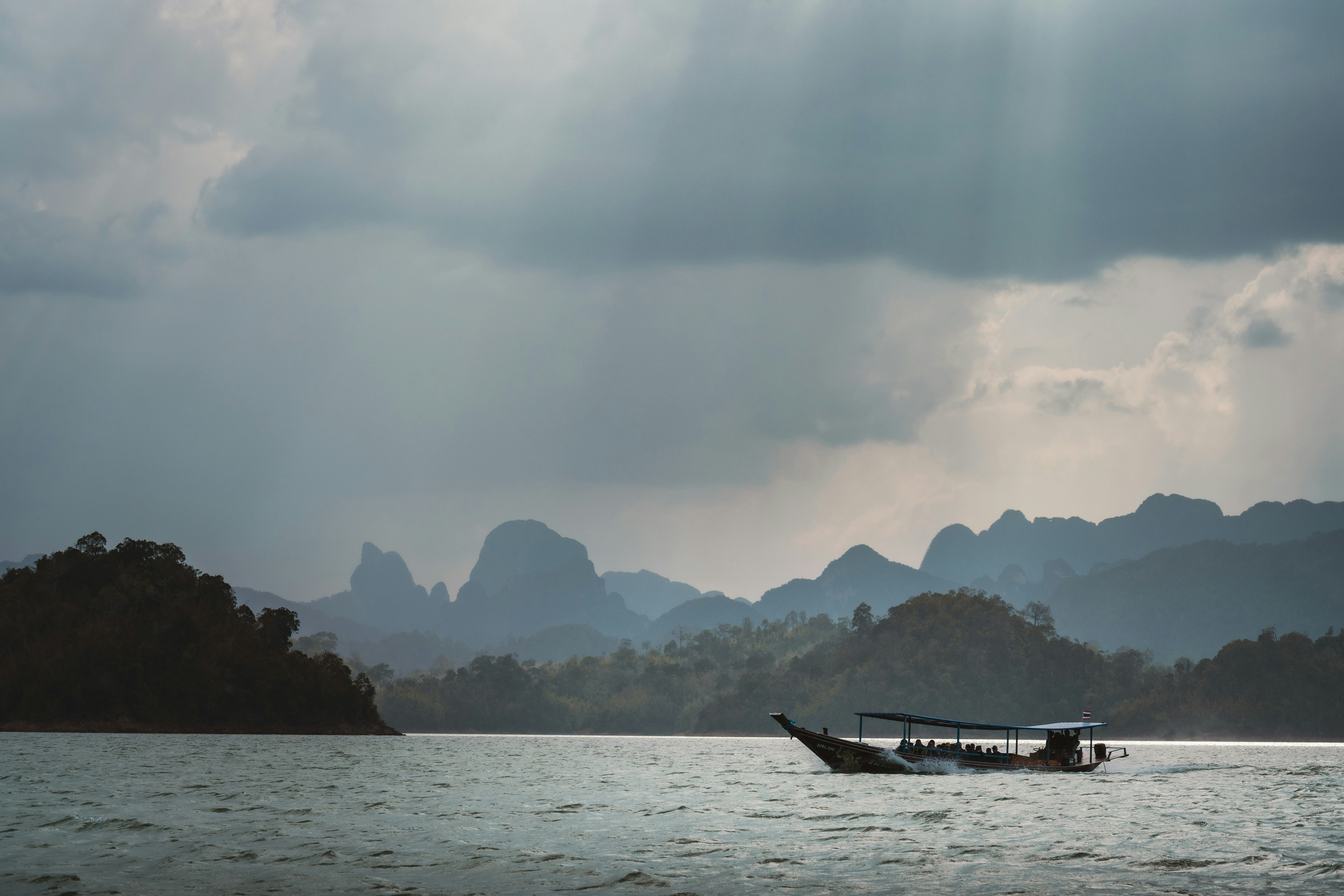 Sunbeams on a Quiet Lake: Boat Silhouette Amid Mountain Backdrop