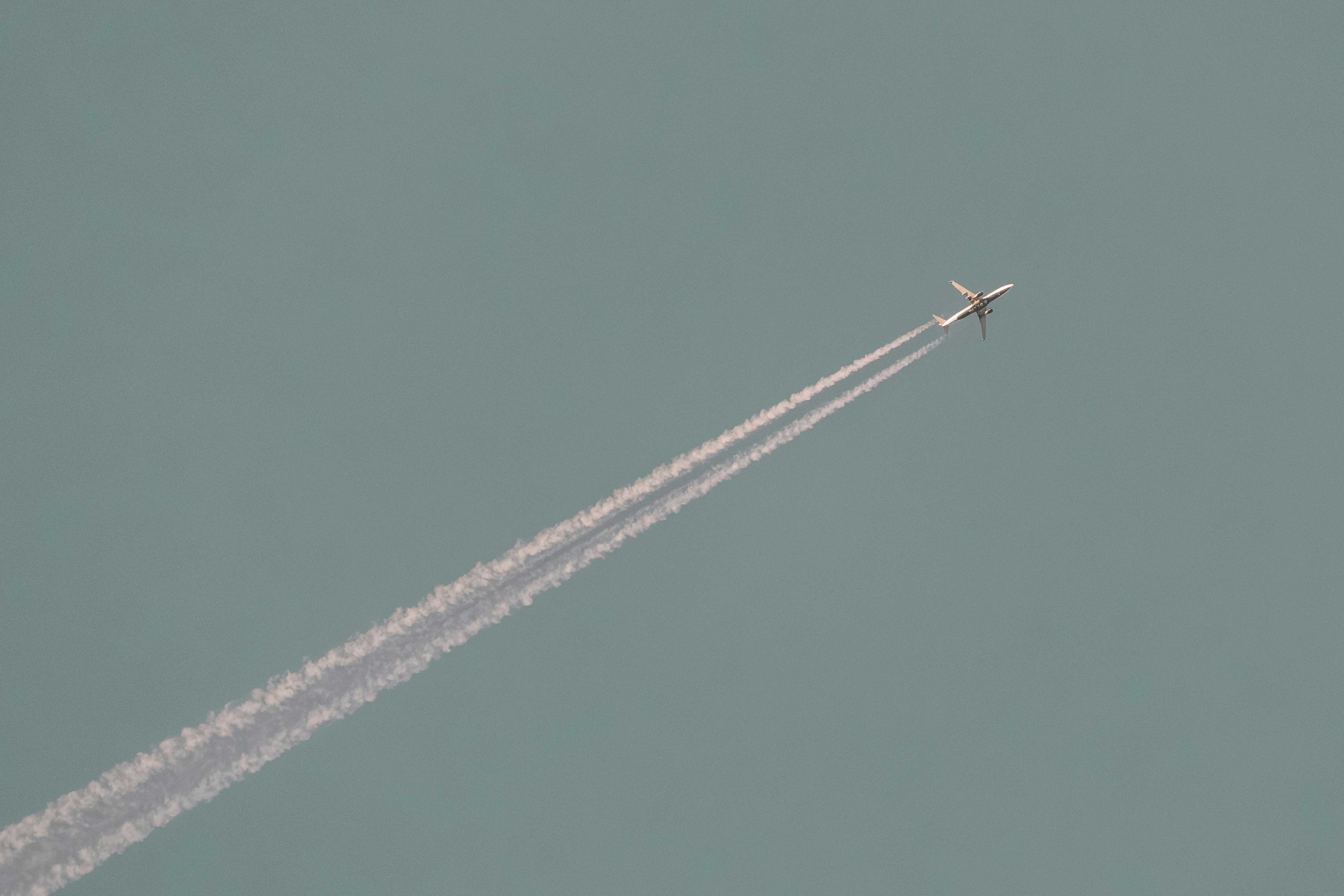 Contrail Conductor: A lone aircraft traces a fresh white wake across a pale blue sky