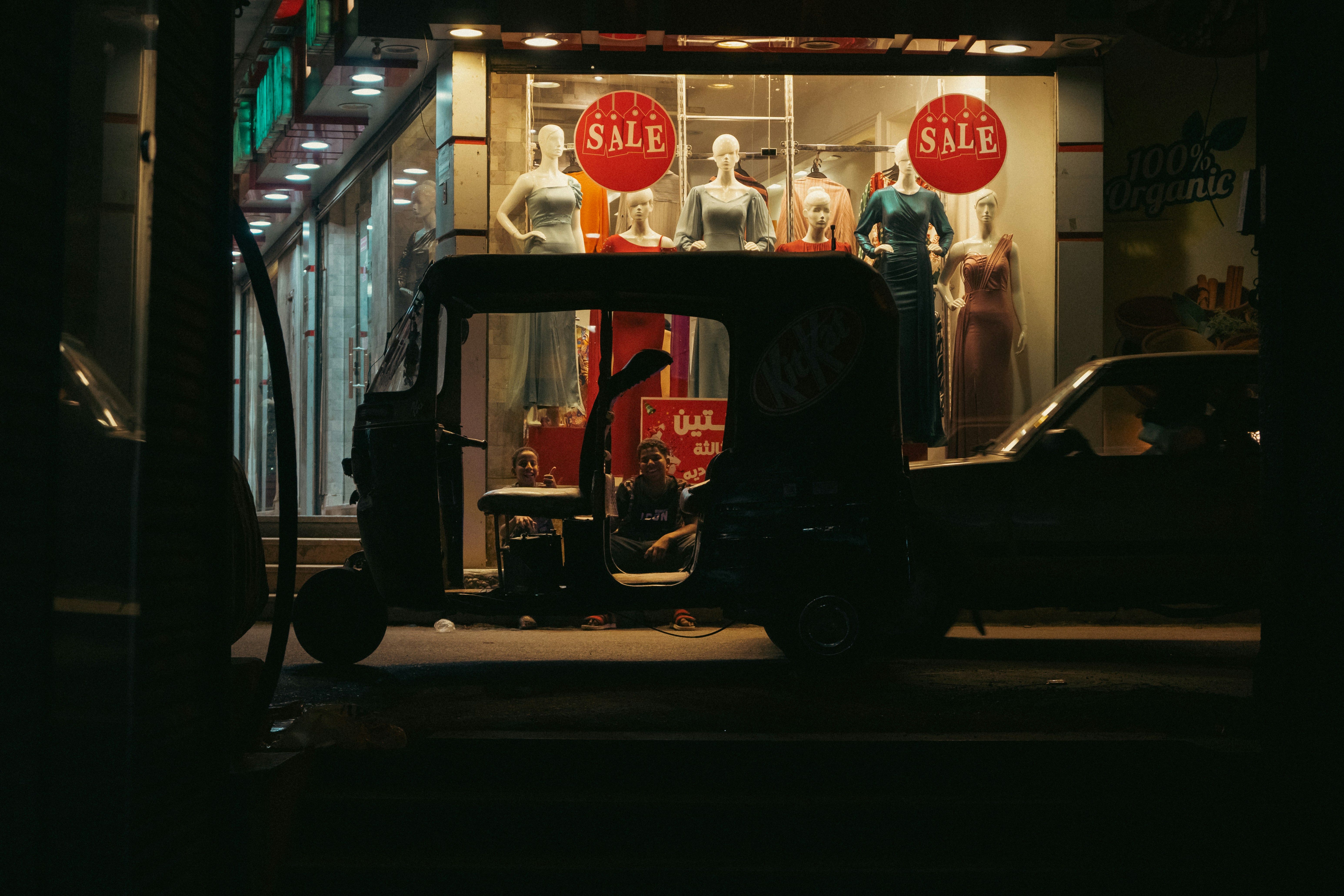 Night Wardrobe: mannequins under sale signs in a dim storefront