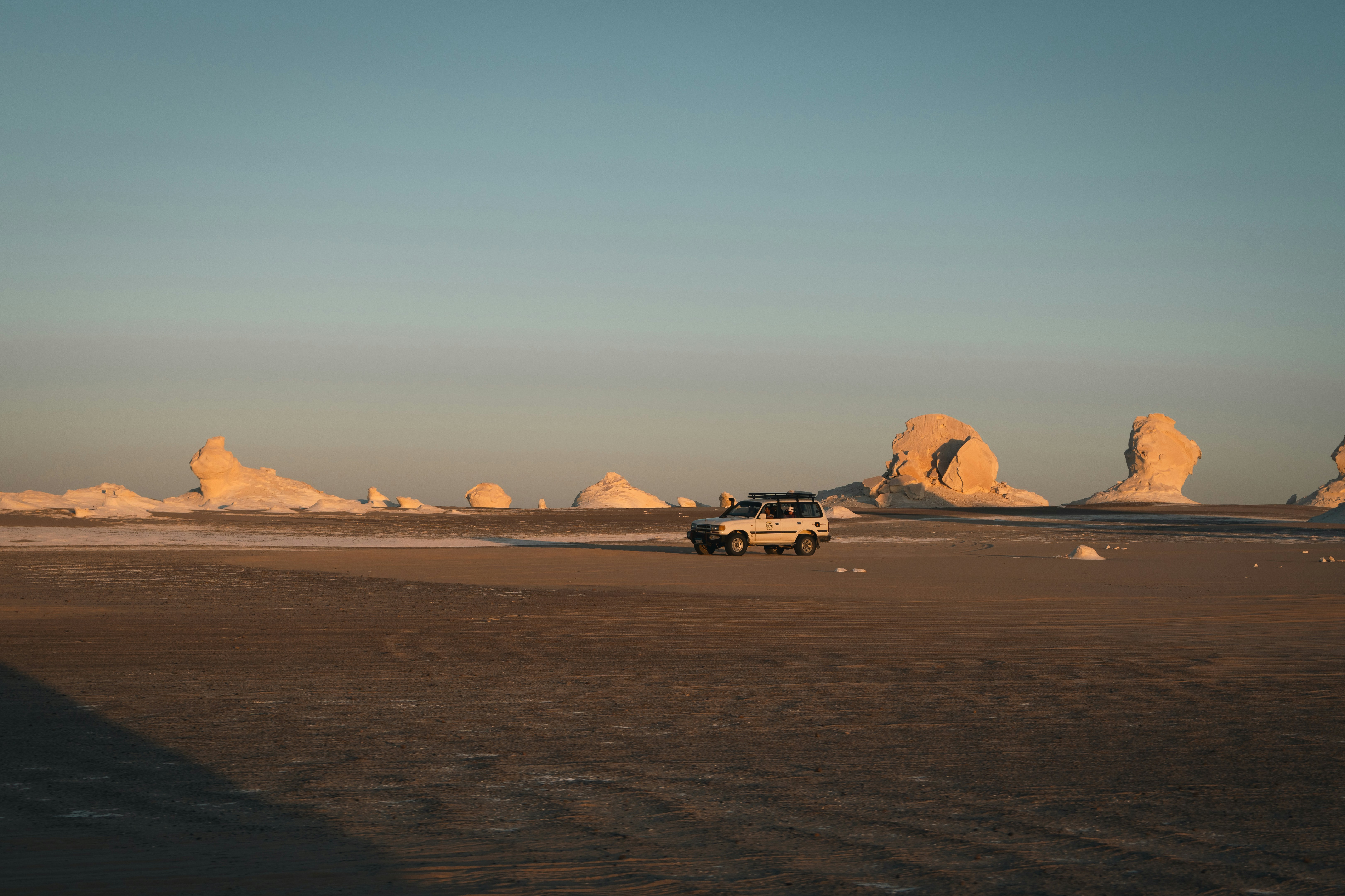 A white suv drives across a desert landscape.