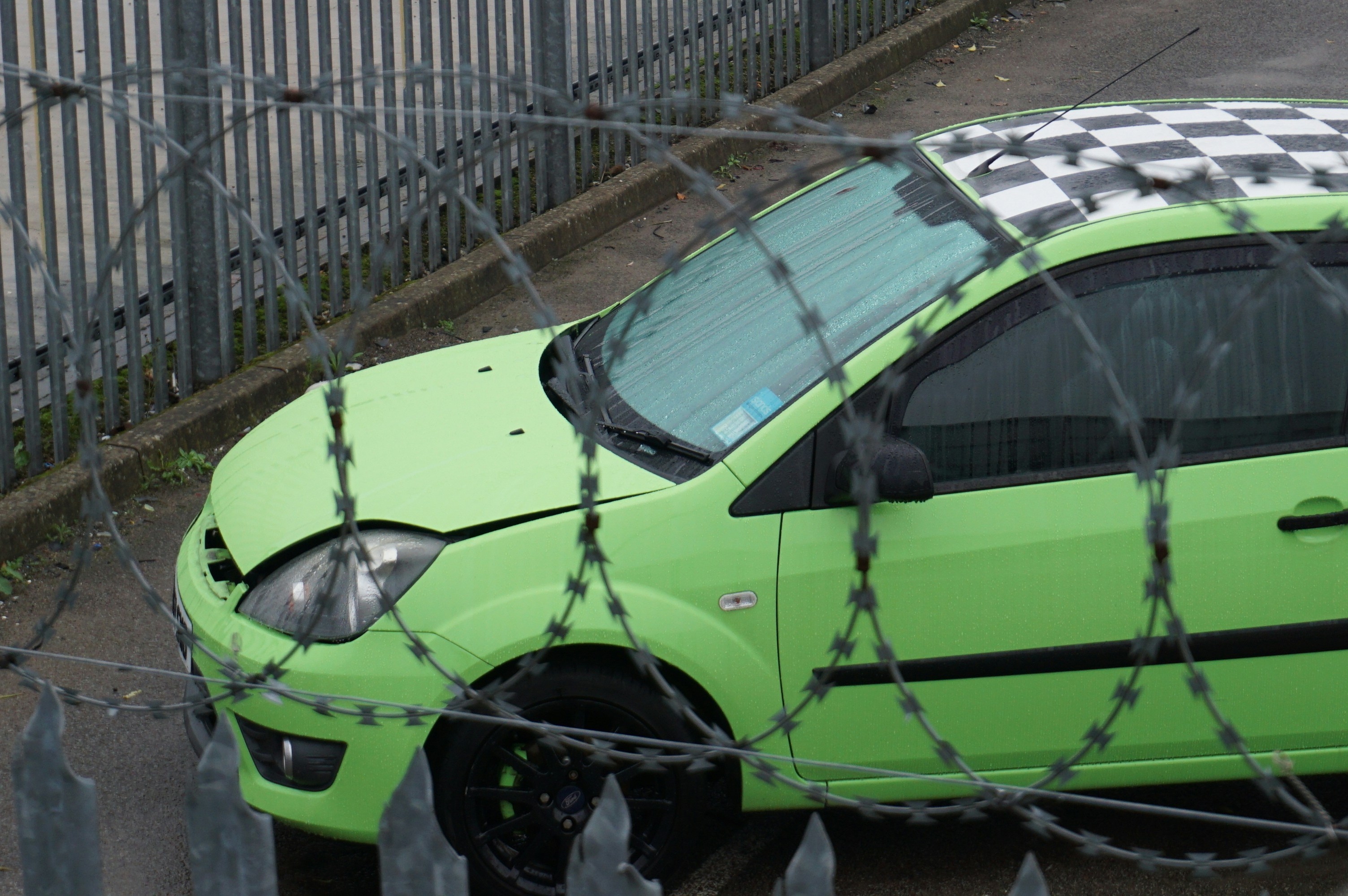 Neon-green hatch under guard: a parked car framed by barbed metal