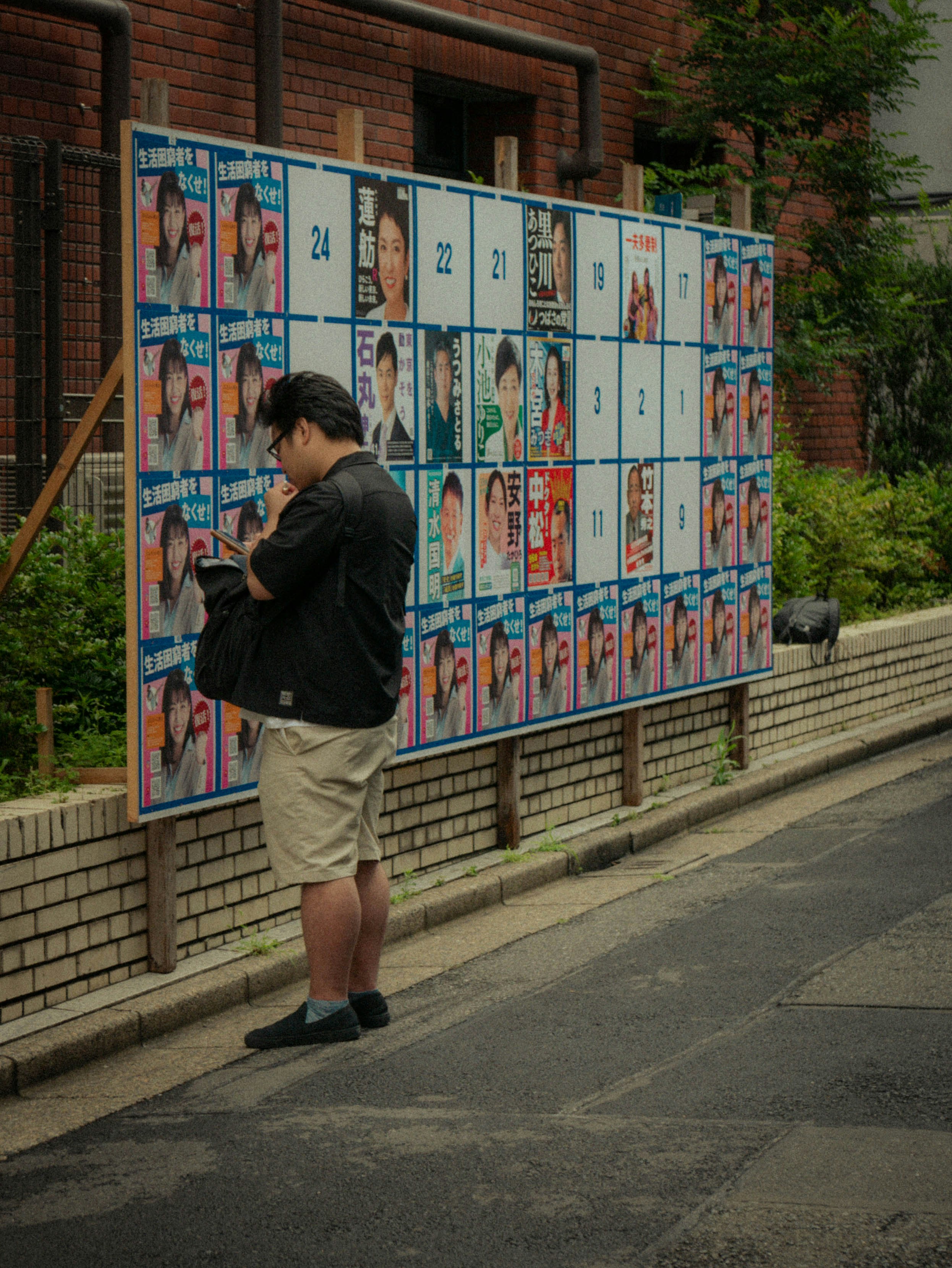 Man with Camera Studying Posters along an Urban Wall
