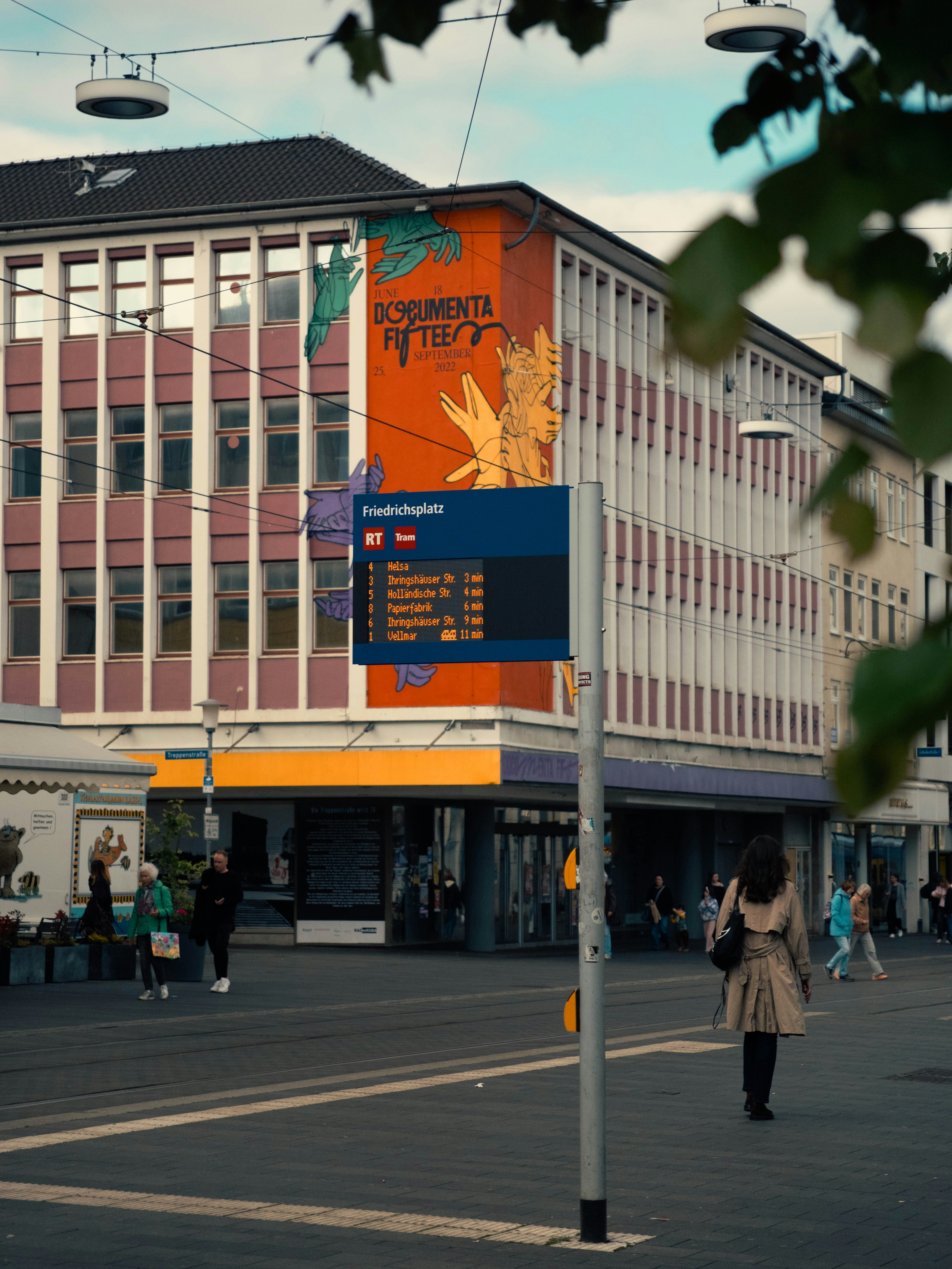 Orange mural on a city building frames the bus stop sign with pedestrians below