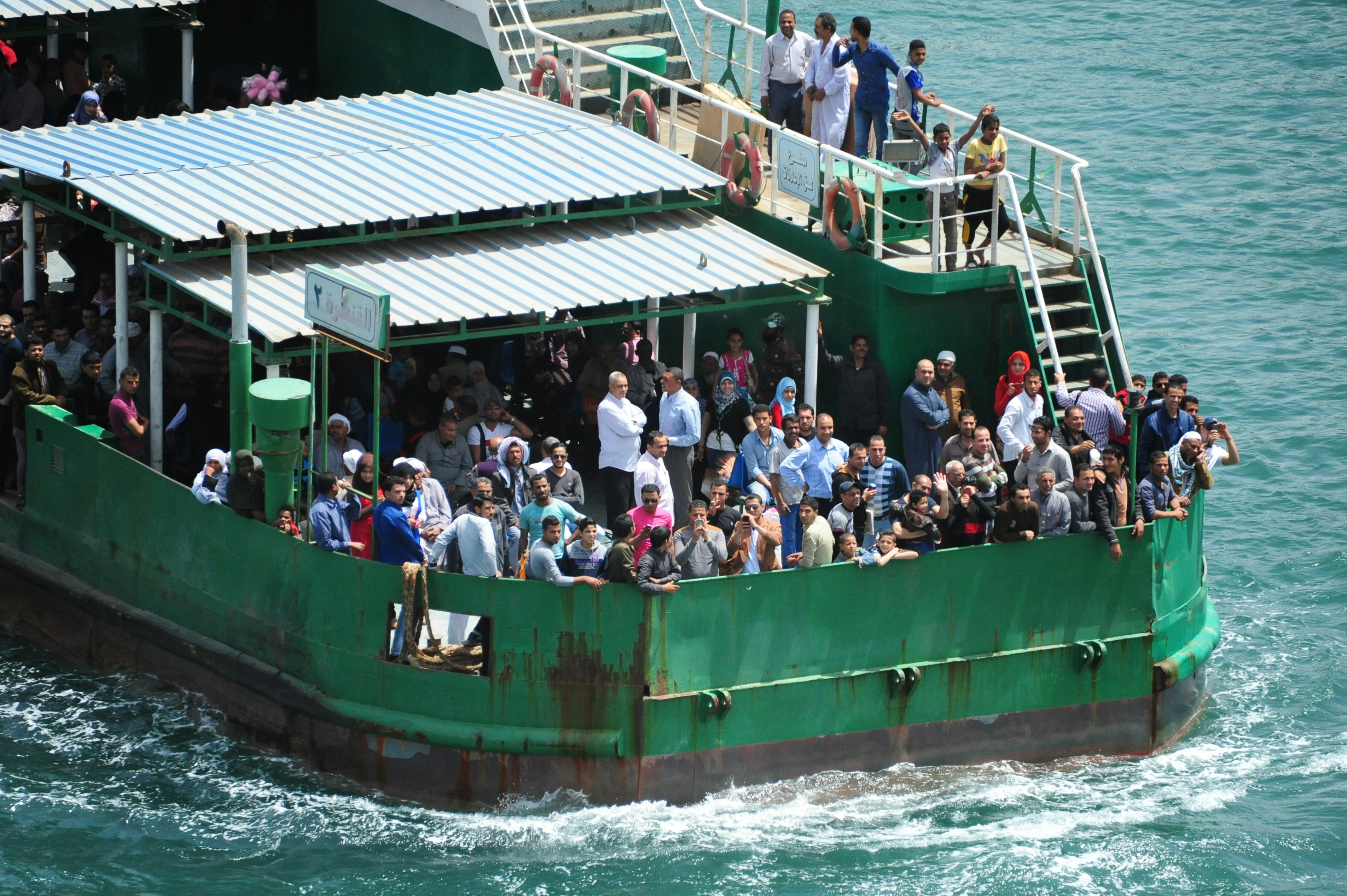 Crowded green ferry surges forward with passengers peering toward the water