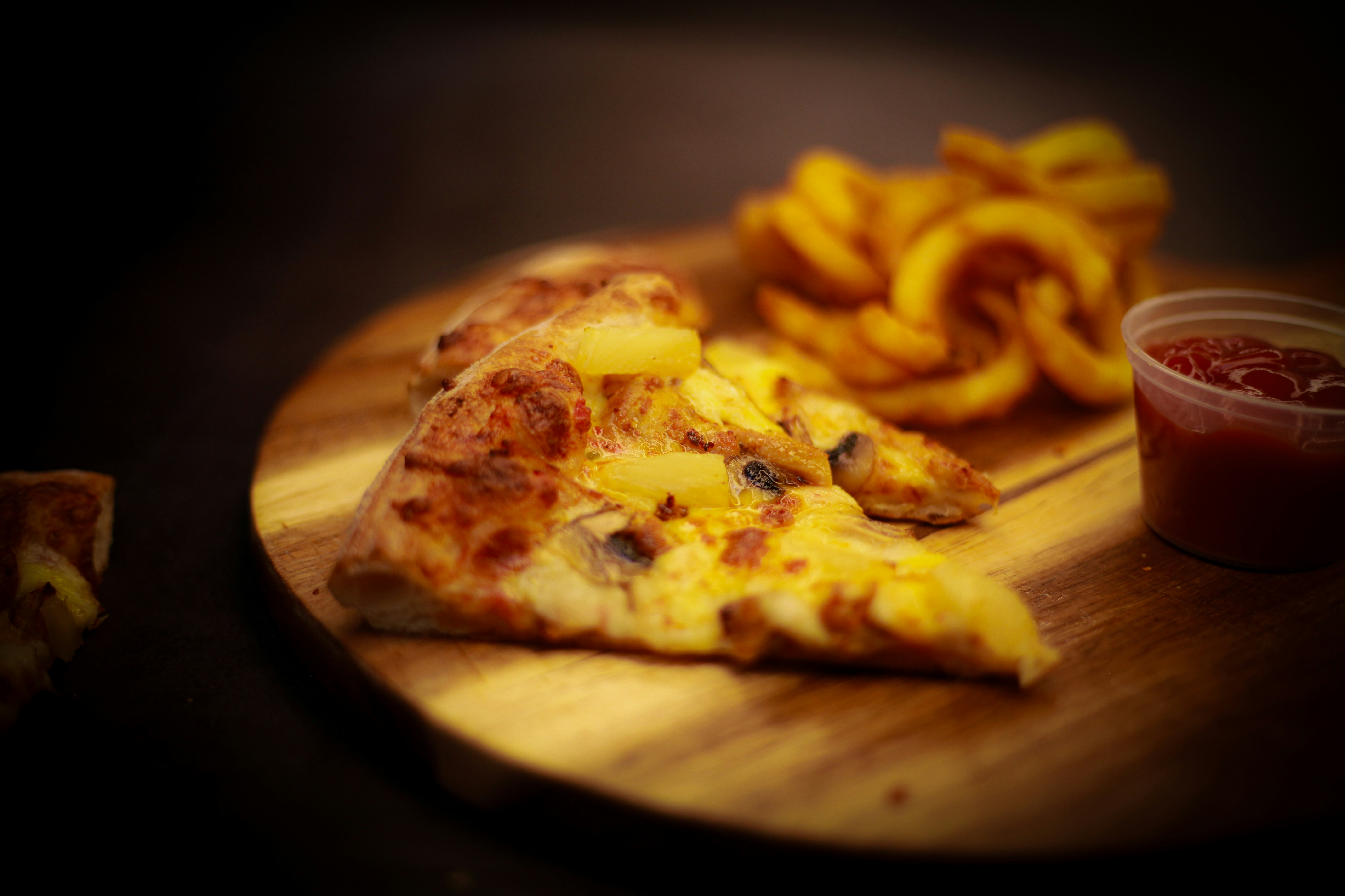 Wooden board with cheesy pizza wedges and a side of sauce under warm, moody lighting