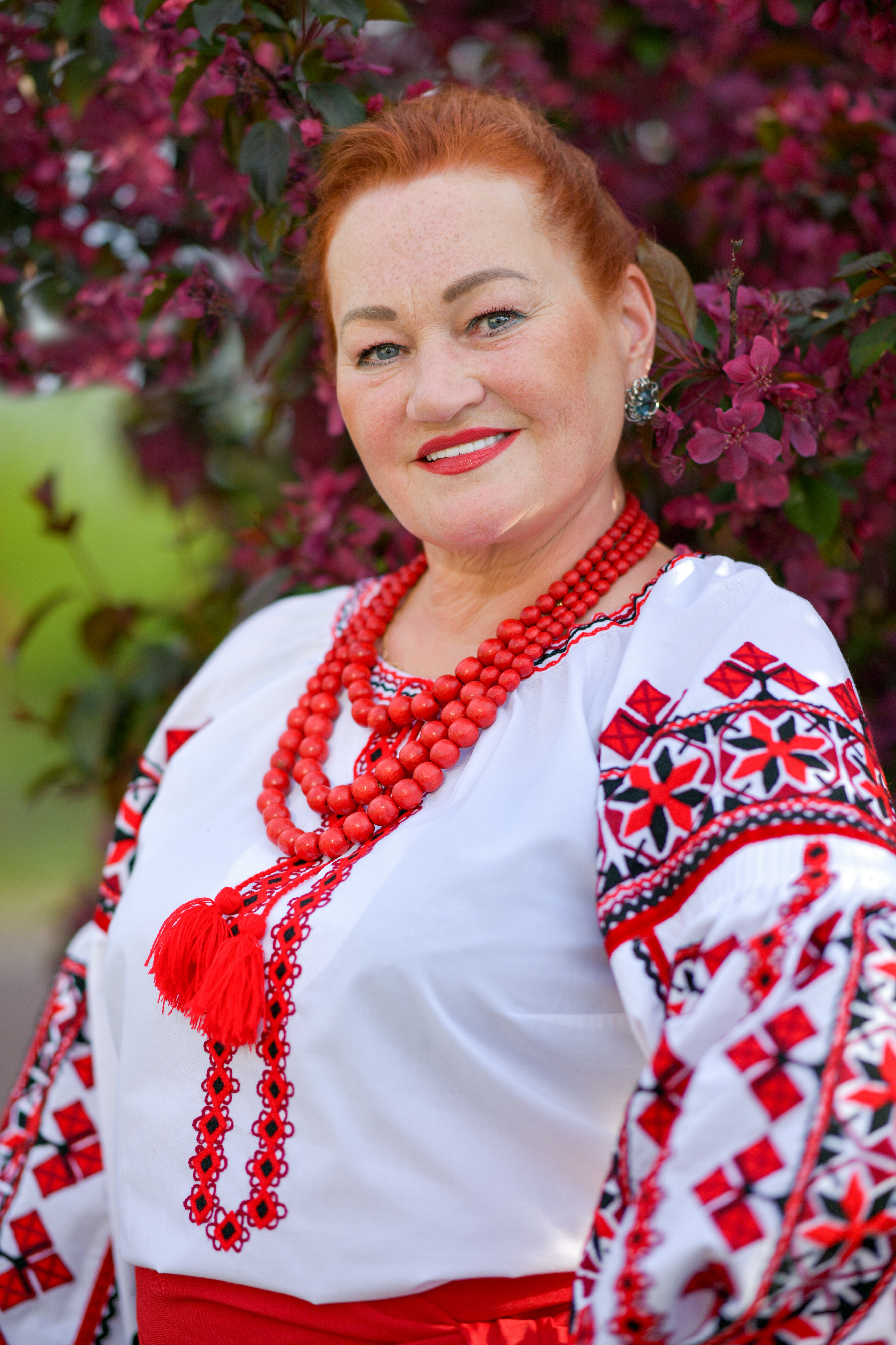 Red Dame in Traditional Embellishments: A Portrait Beneath Fuchsia Blossoms