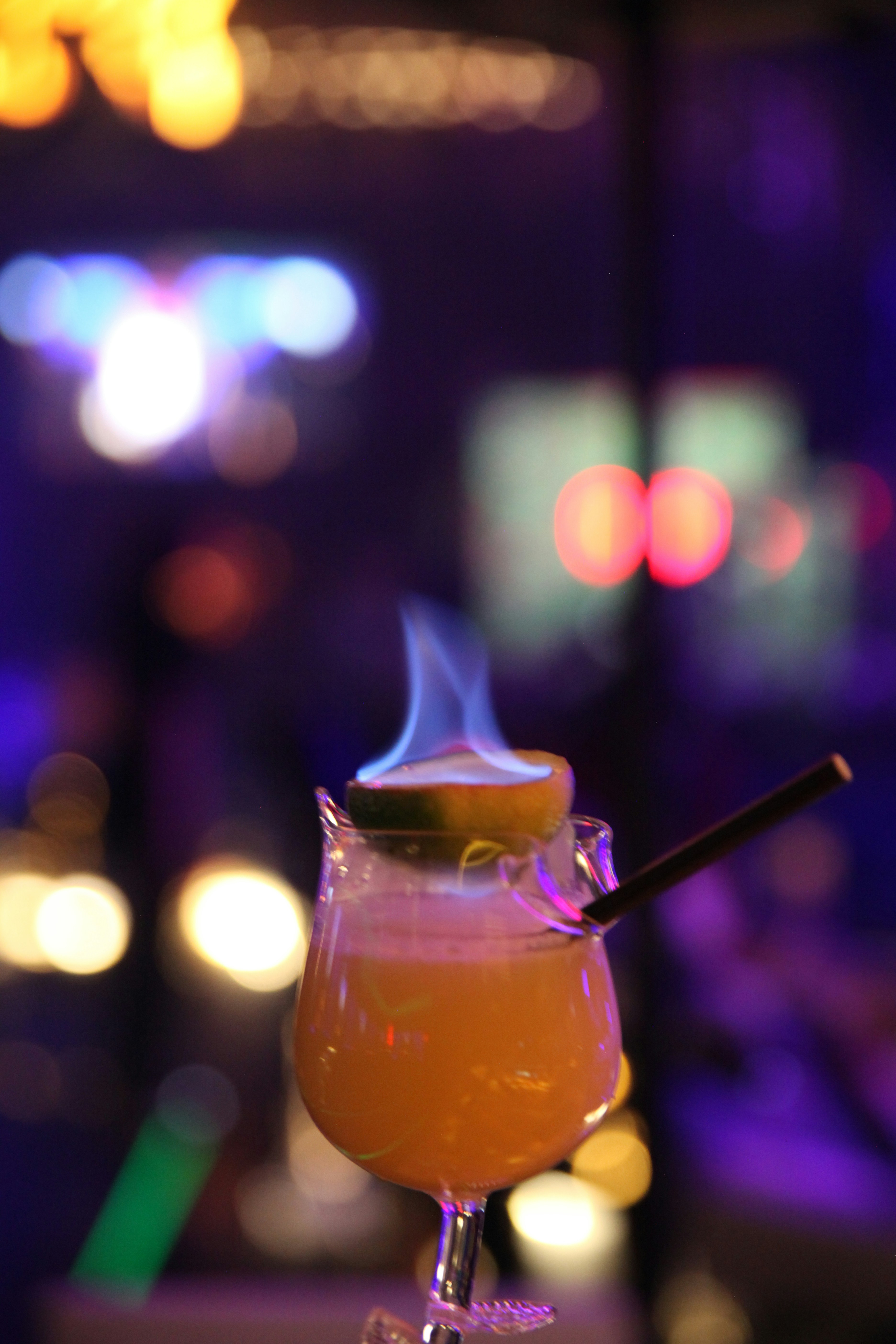 Blue-flamed cocktail under neon glow in a bustling bar