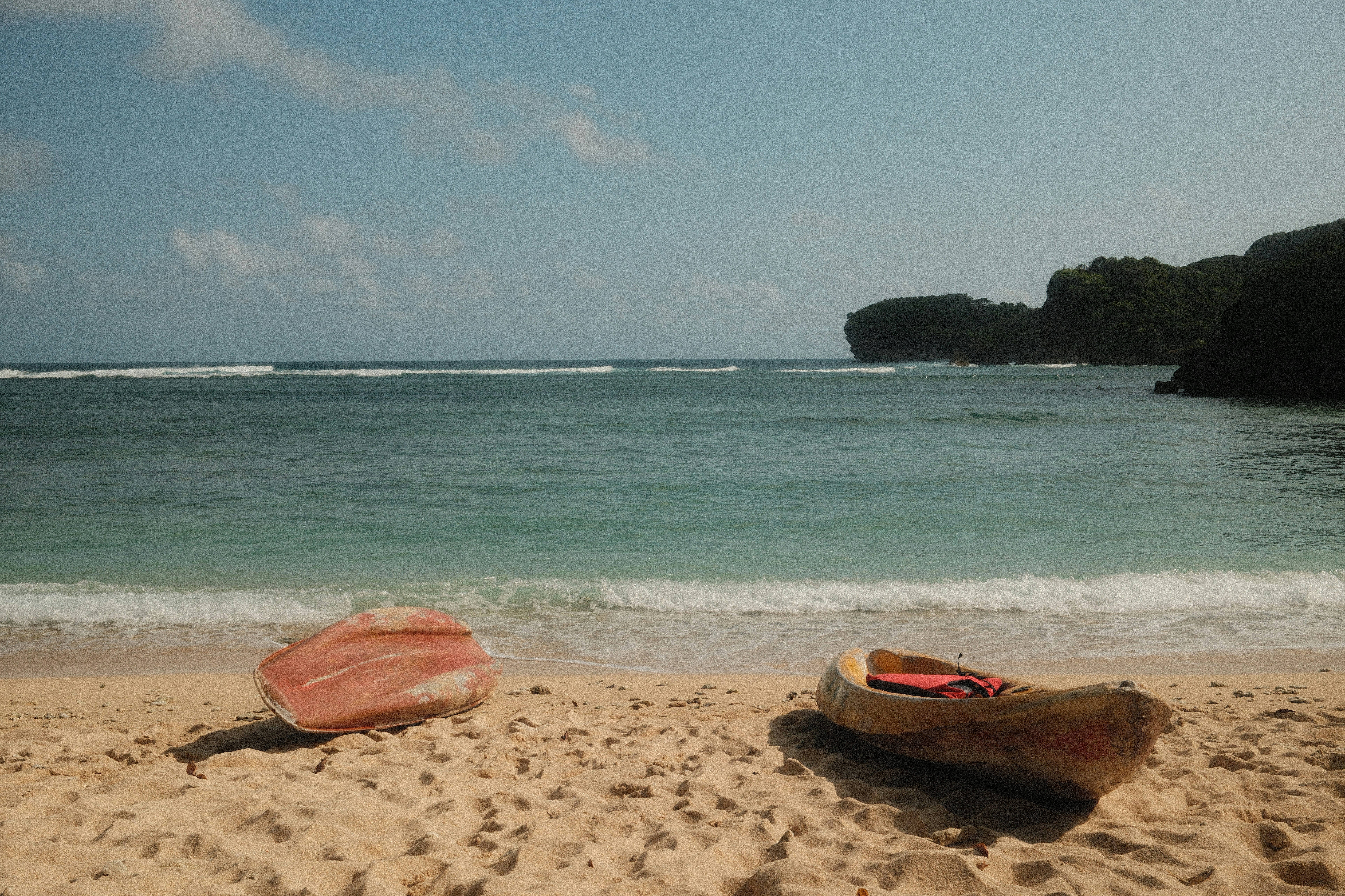Two weathered kayaks rest on sunlit sand as turquoise waves kiss a quiet shore