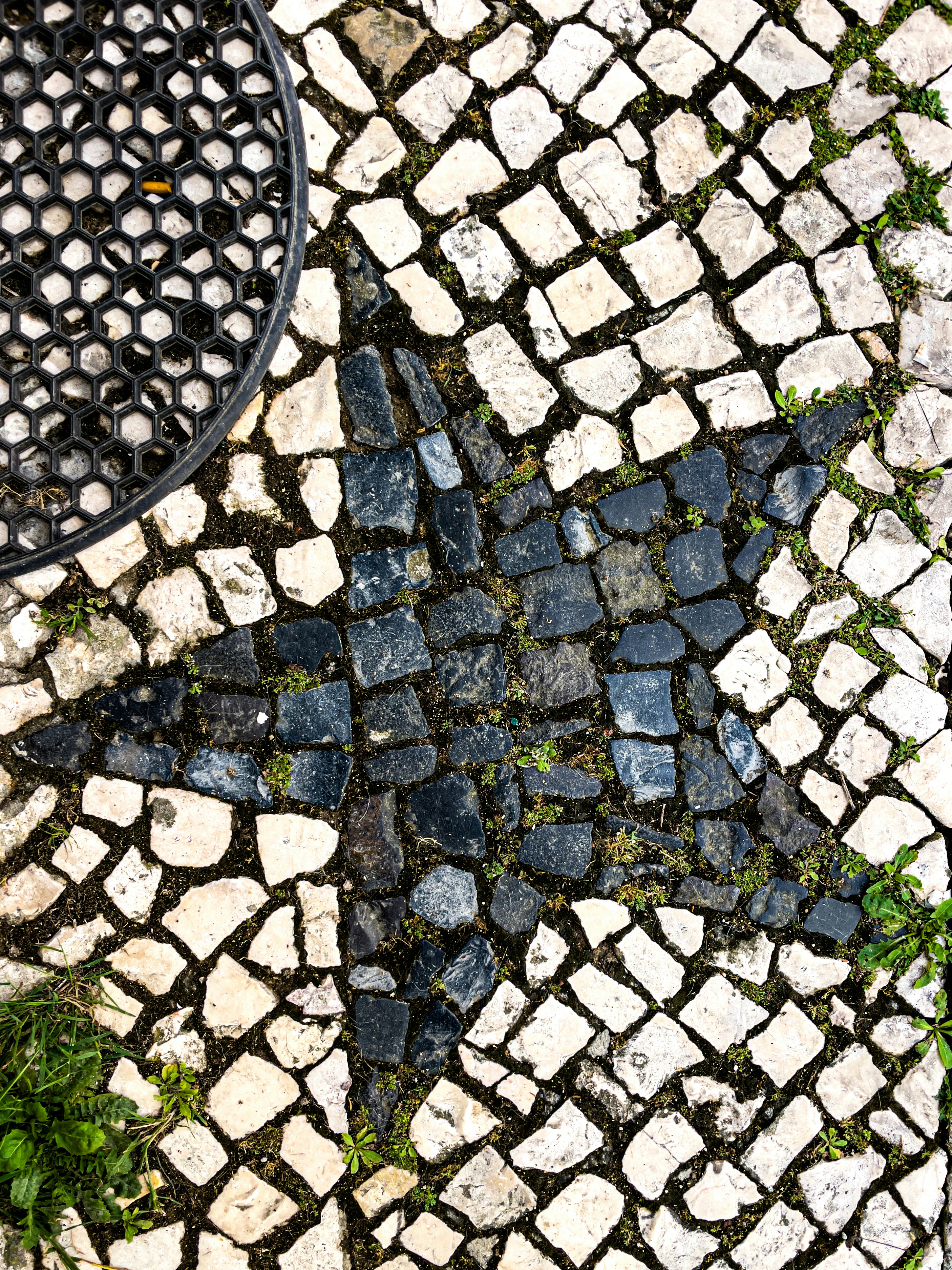 Stone mosaic drain: a circular grate meets a cobblestone crosswalk