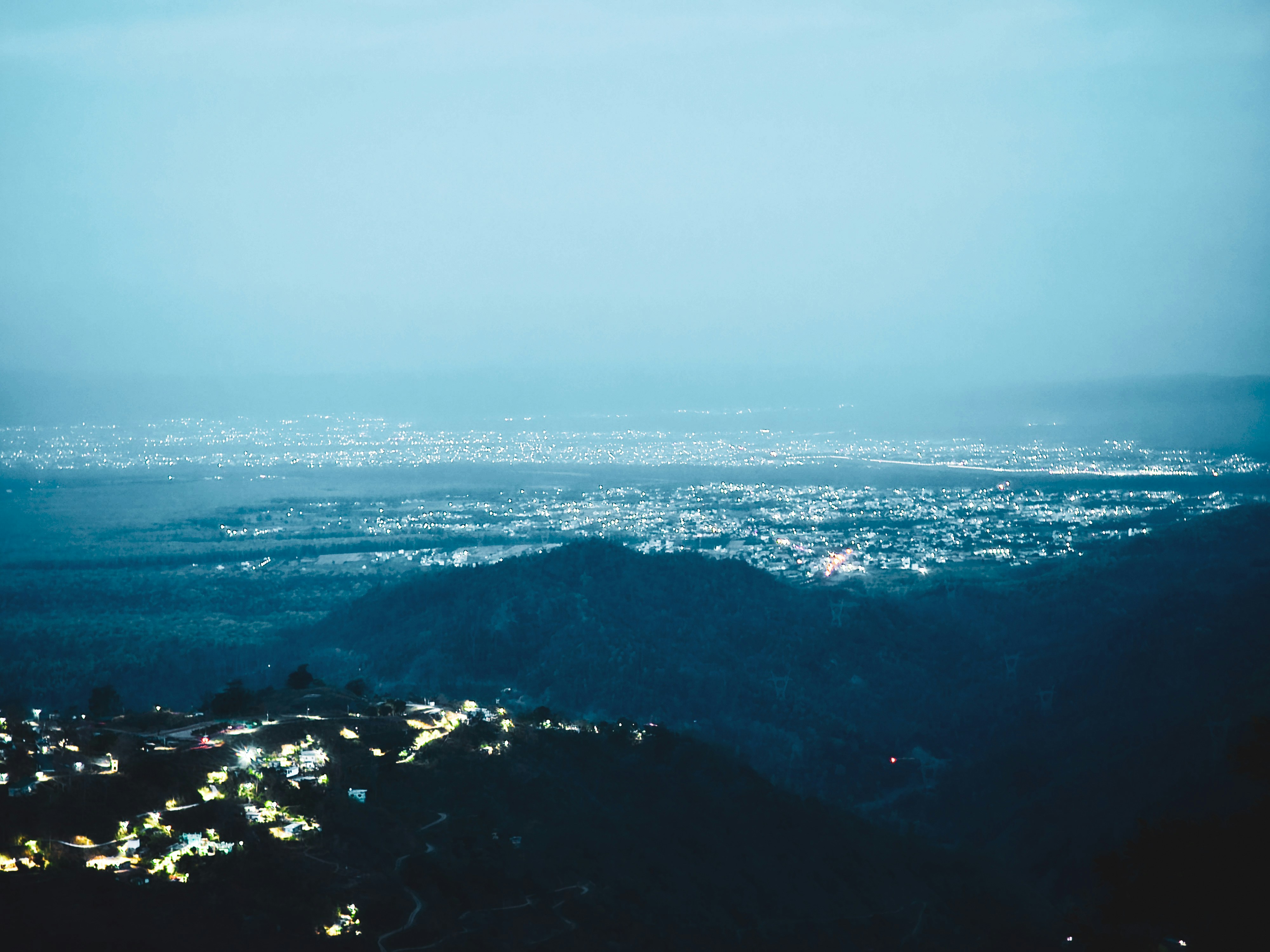 Luminous Valley: City Lights Nestled Beyond the Hills at Dusk