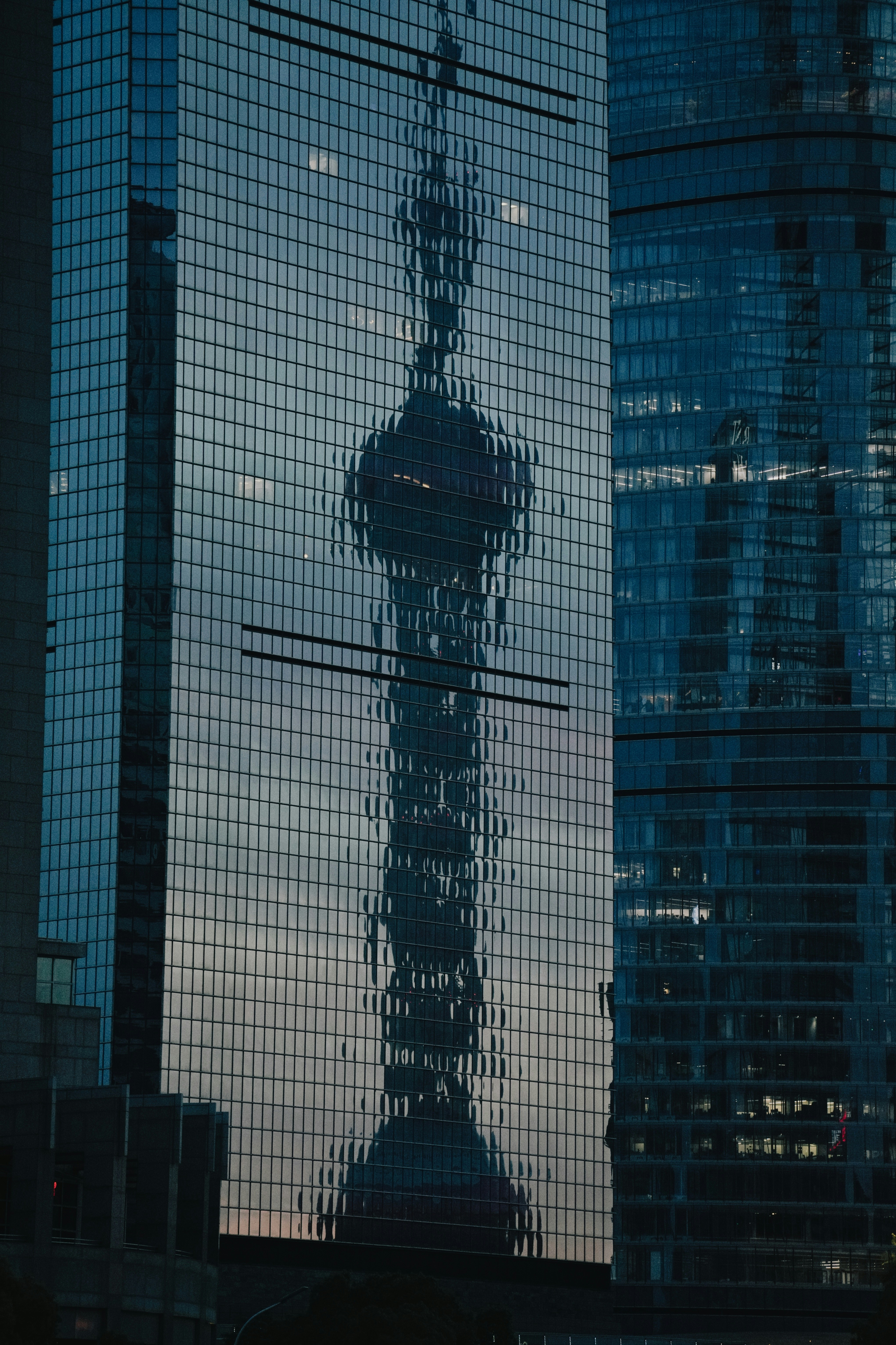 Modern skyscraper reflecting a distant tower at dusk