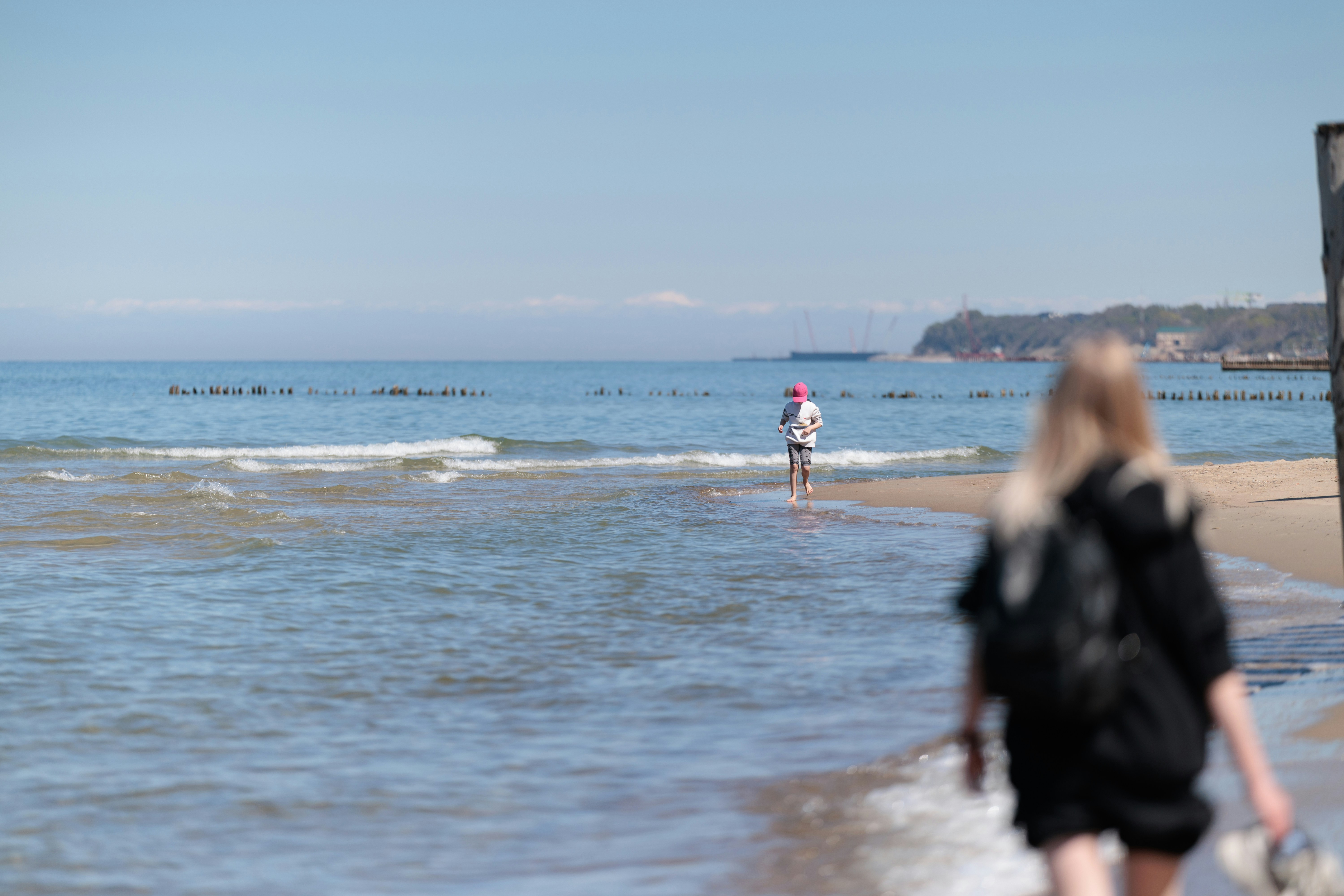 Far Shore Wanderer: a lone angler at the waterline foregrounded by a passing walker