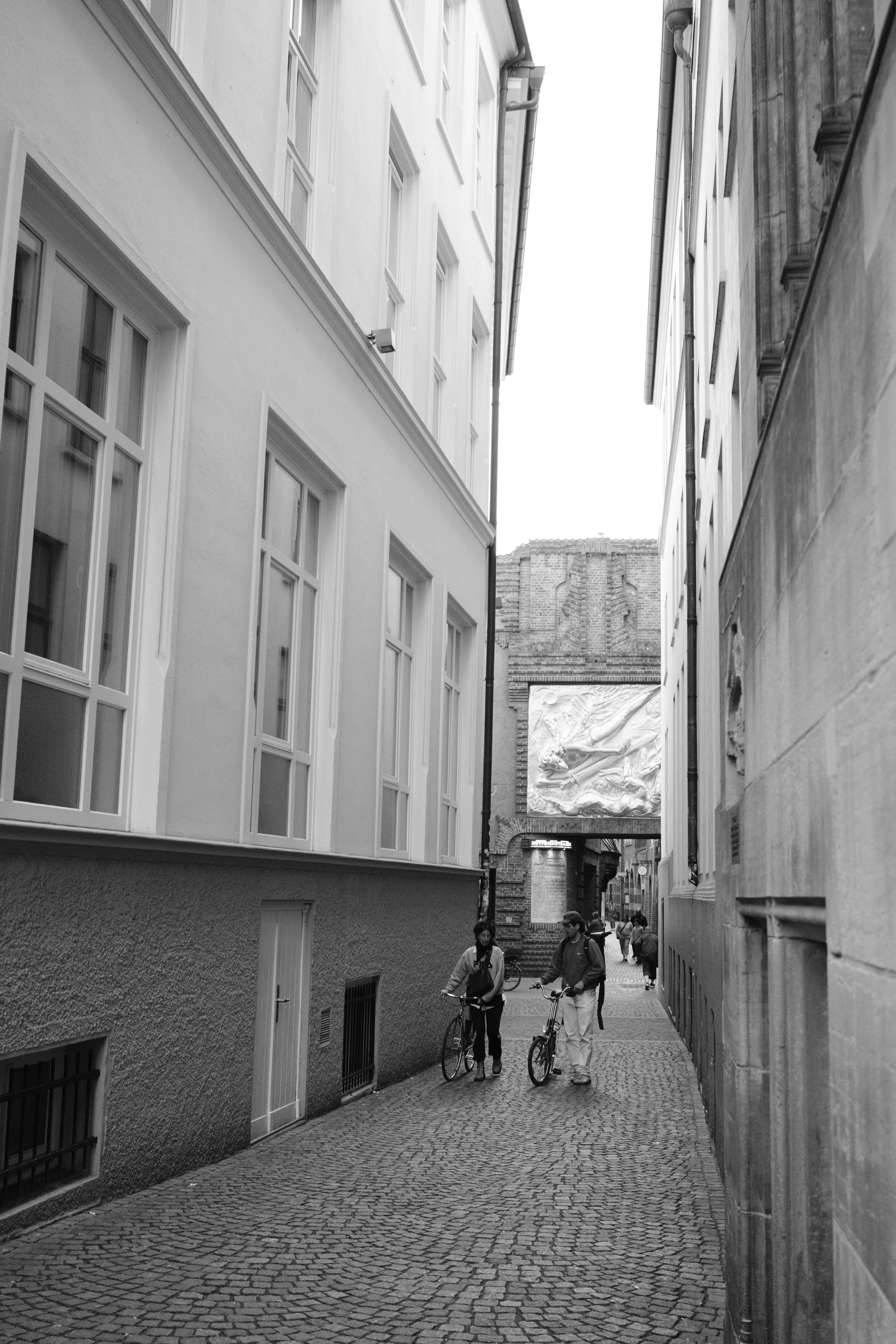 Cobbled Alley Convergence: Cyclists in Narrow Stone Passage