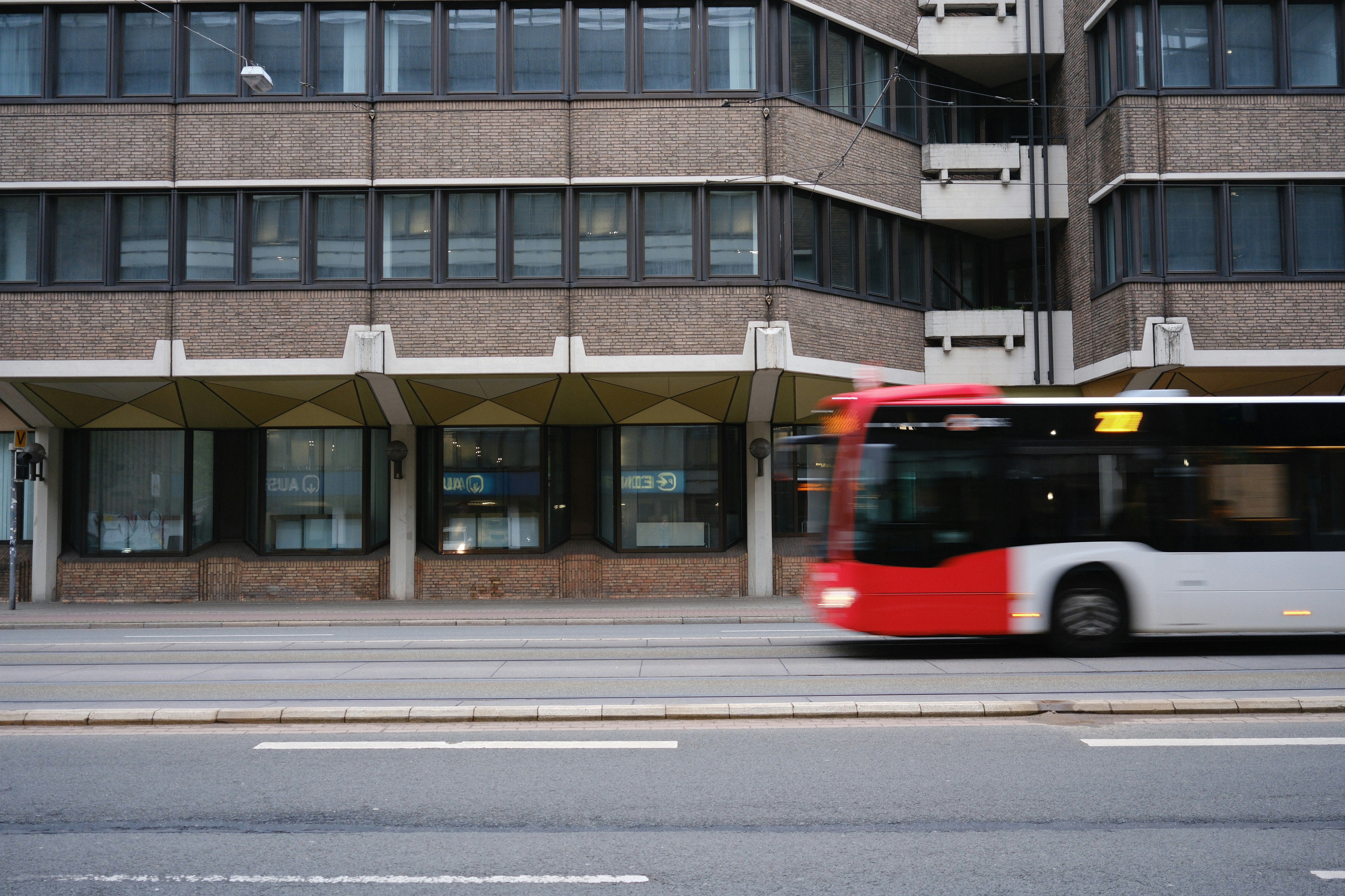 Red City Bus in Motion Past a Brutalist Facade