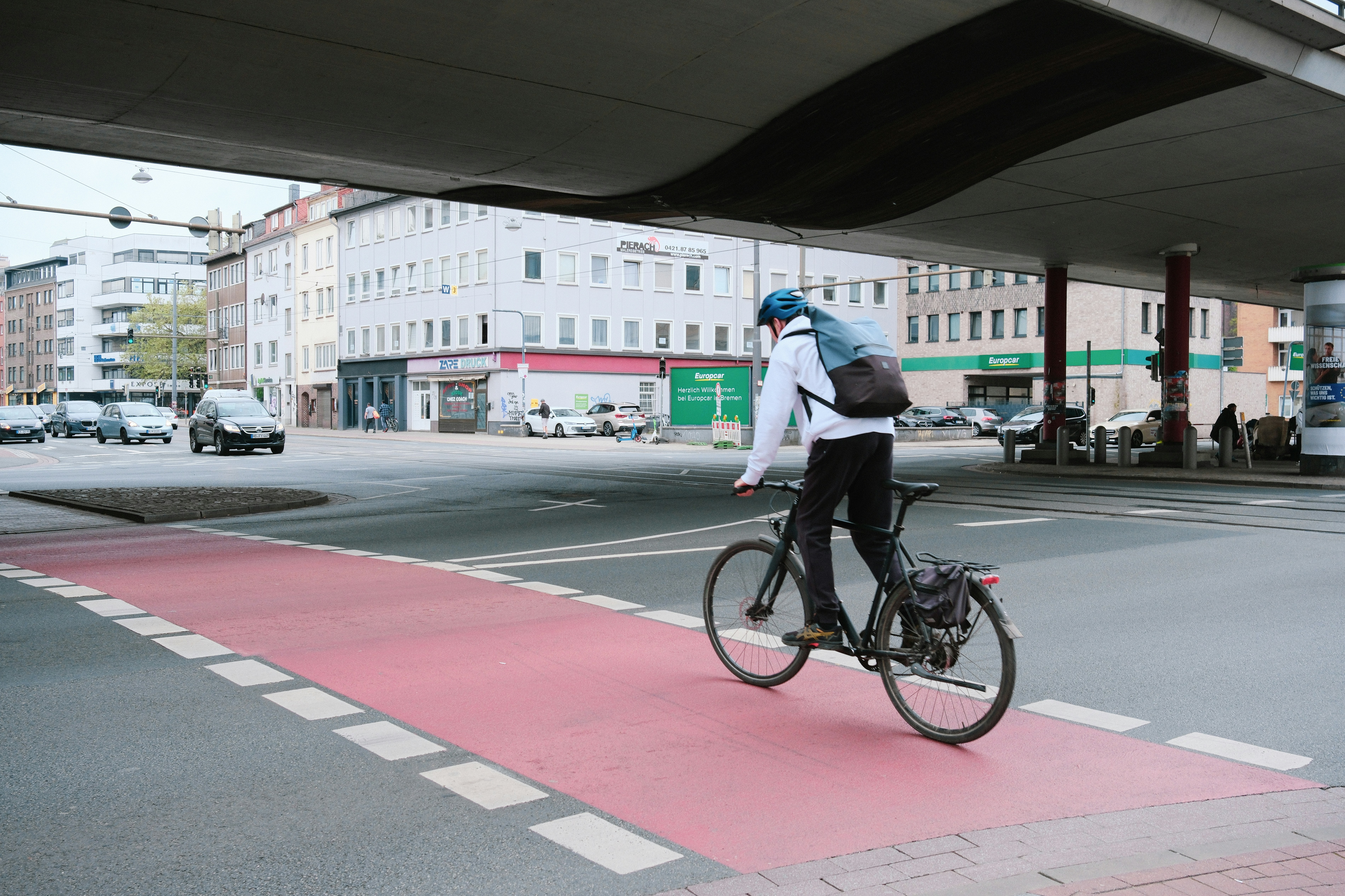 Cyclist Crossing a Red-Paved Path Under an Urban Overpass