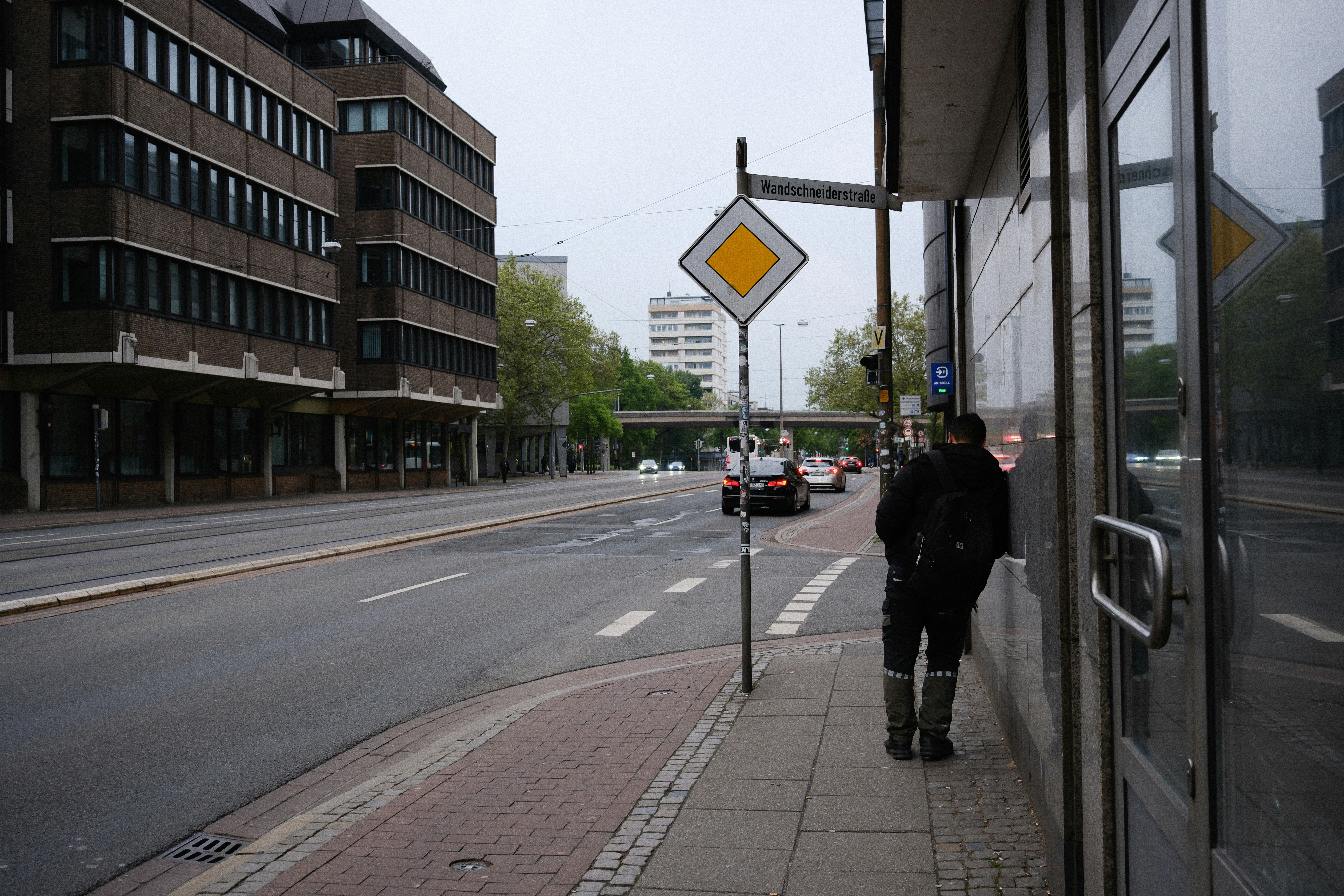 Sidewalk Vigil: A Pedestrian Stands by the Glass Frontage