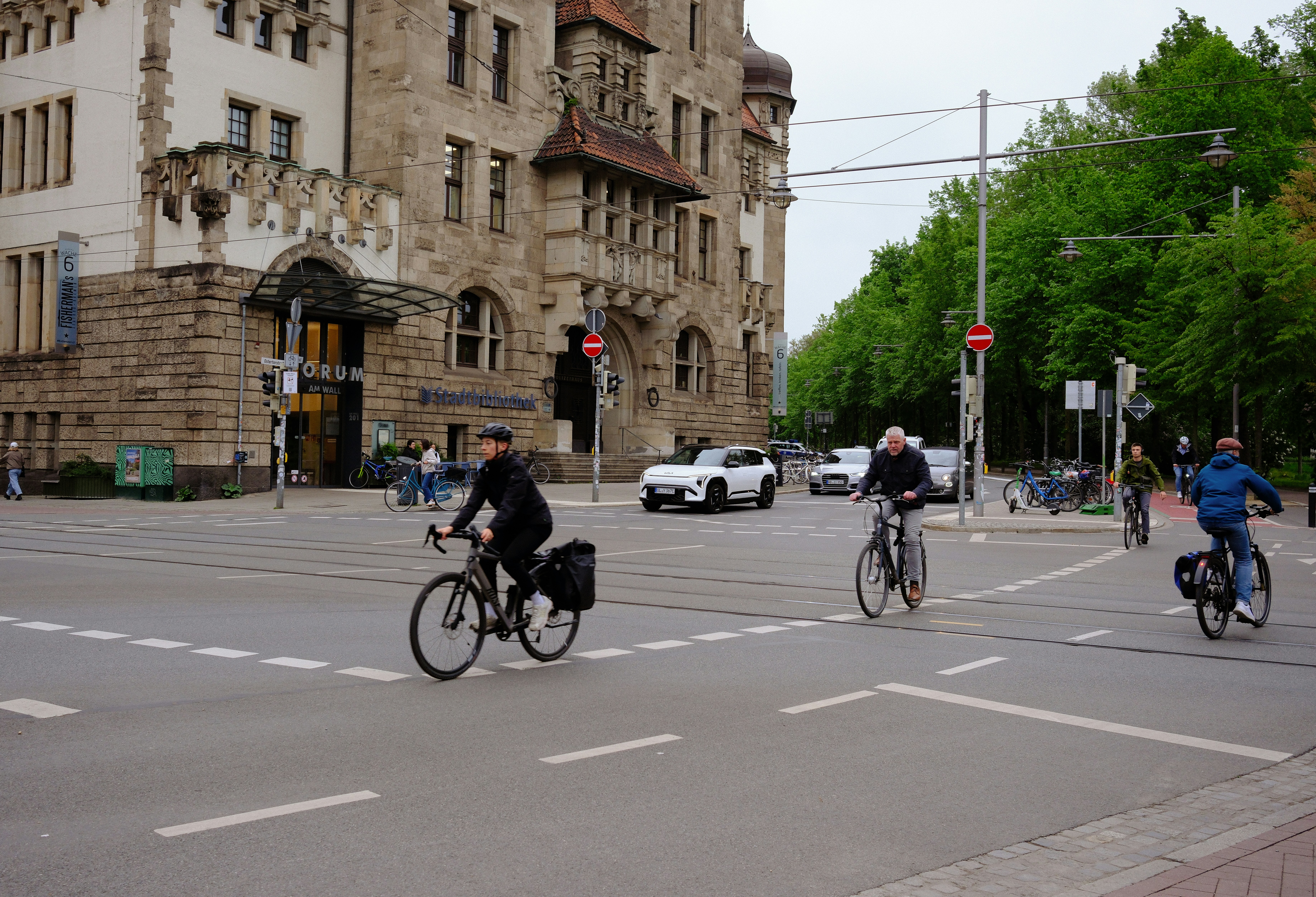 City crosswalk vigil: cyclists glide past an ornate stone building
