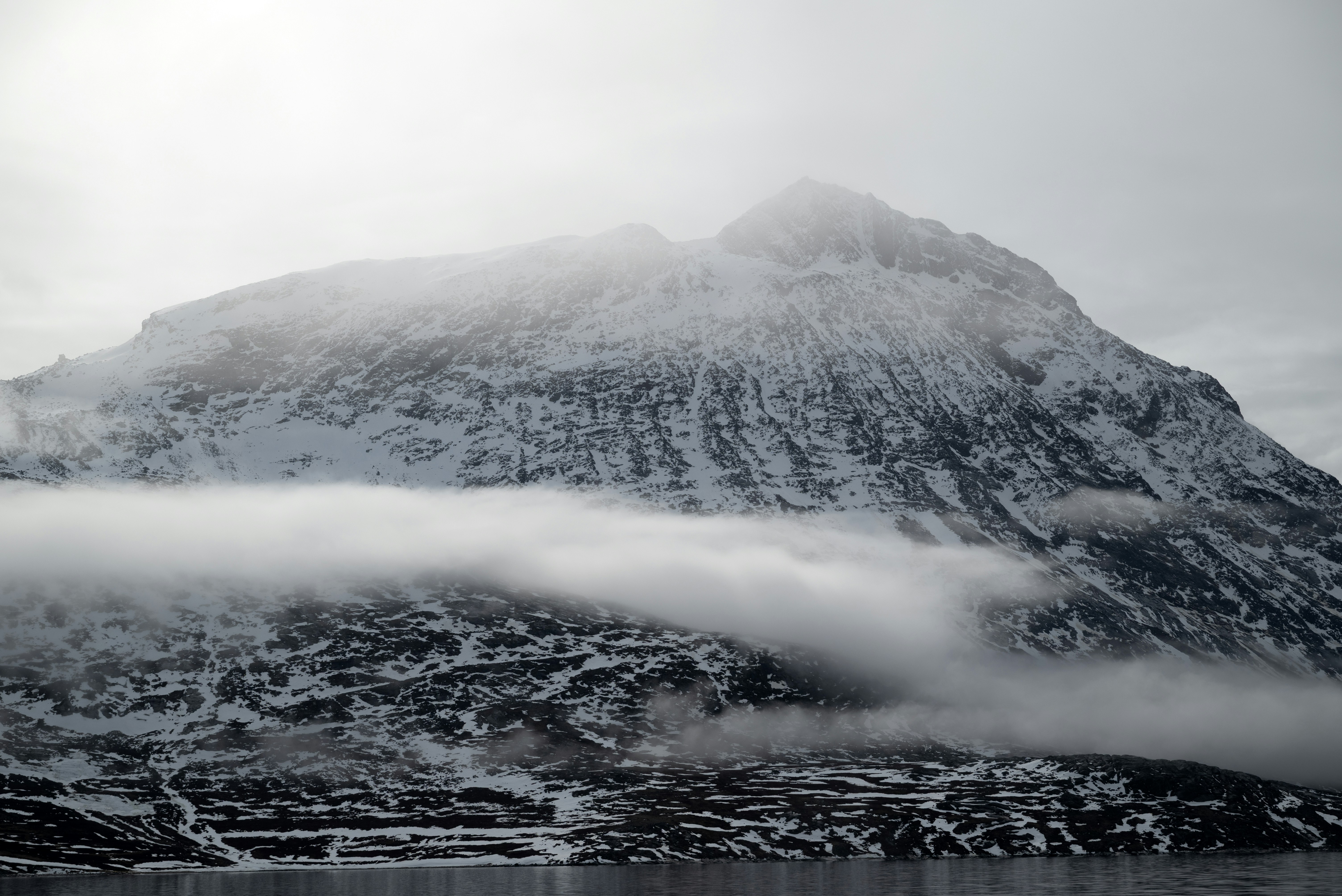 Mist-veiled Summit: A Snow-kissed Peak Emerging Through Low Clouds