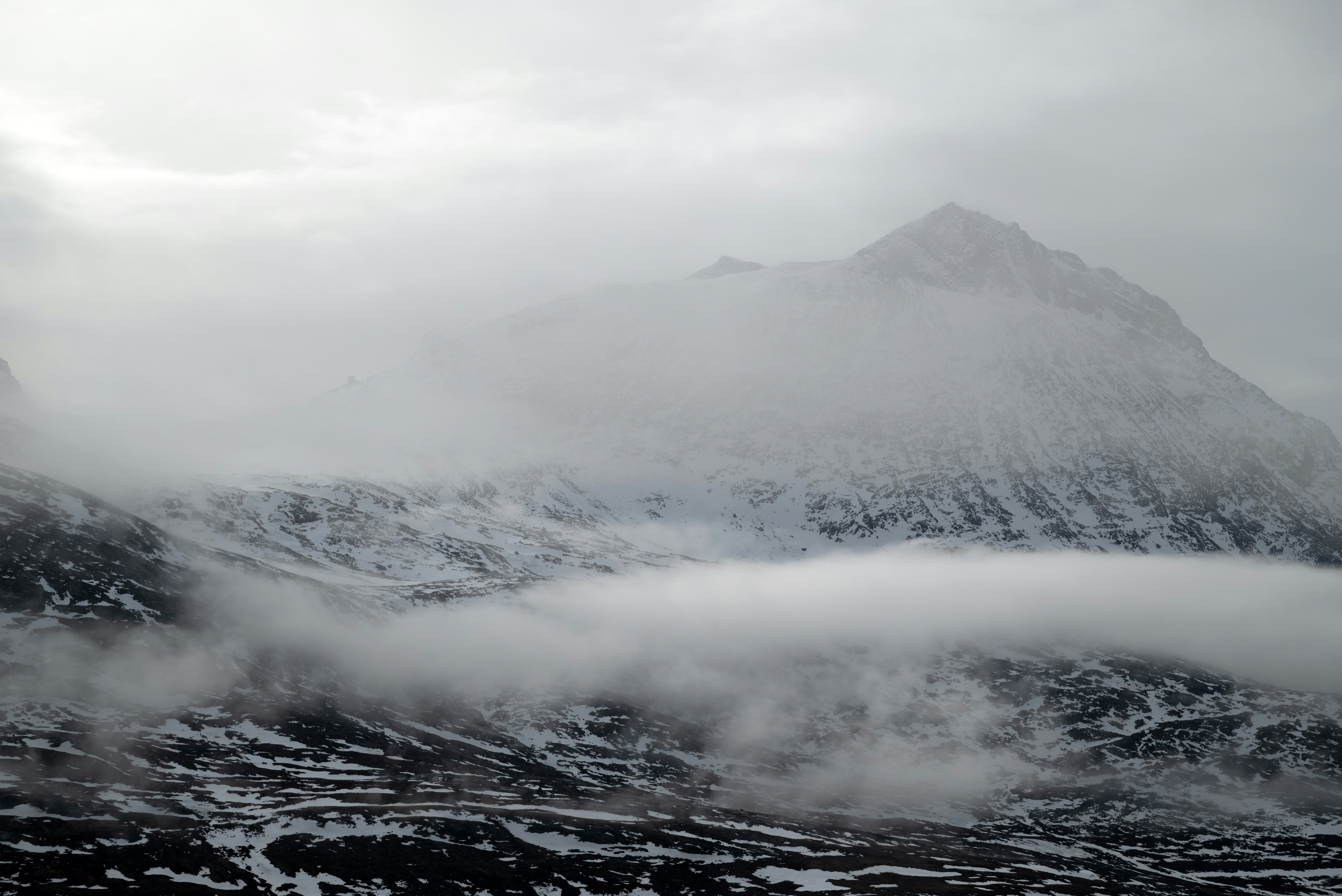 Mist-Wrapped Summit: A Snow-Scarred Peak Emerges through Low-Cloud Veil