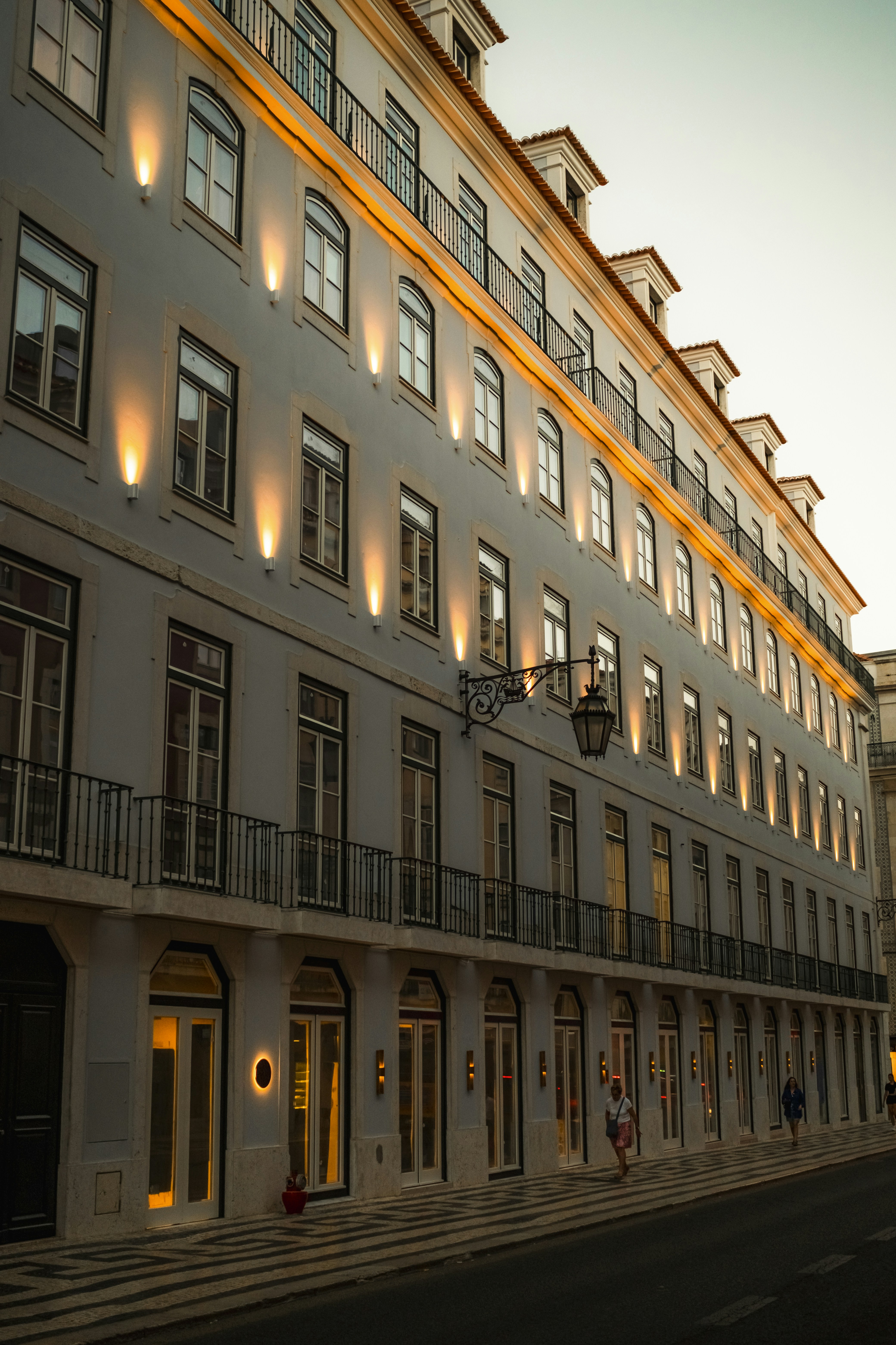 A refined illuminated facade along Rua Áurea in downtown Lisbon, where elegant symmetry, soft architectural lighting, and traditional Portuguese paving stones define the atmosphere of the Baixa district at dusk. Shot in Summer 2025 with Fujifilm X-M5 and Viltrox 25/1.7. // Uma fachada elegantemente iluminada na Rua Áurea, no centro de Lisboa, onde a simetria arquitetónica, a iluminação suave e a tradicional calçada portuguesa definem a atmosfera da Baixa ao entardecer.