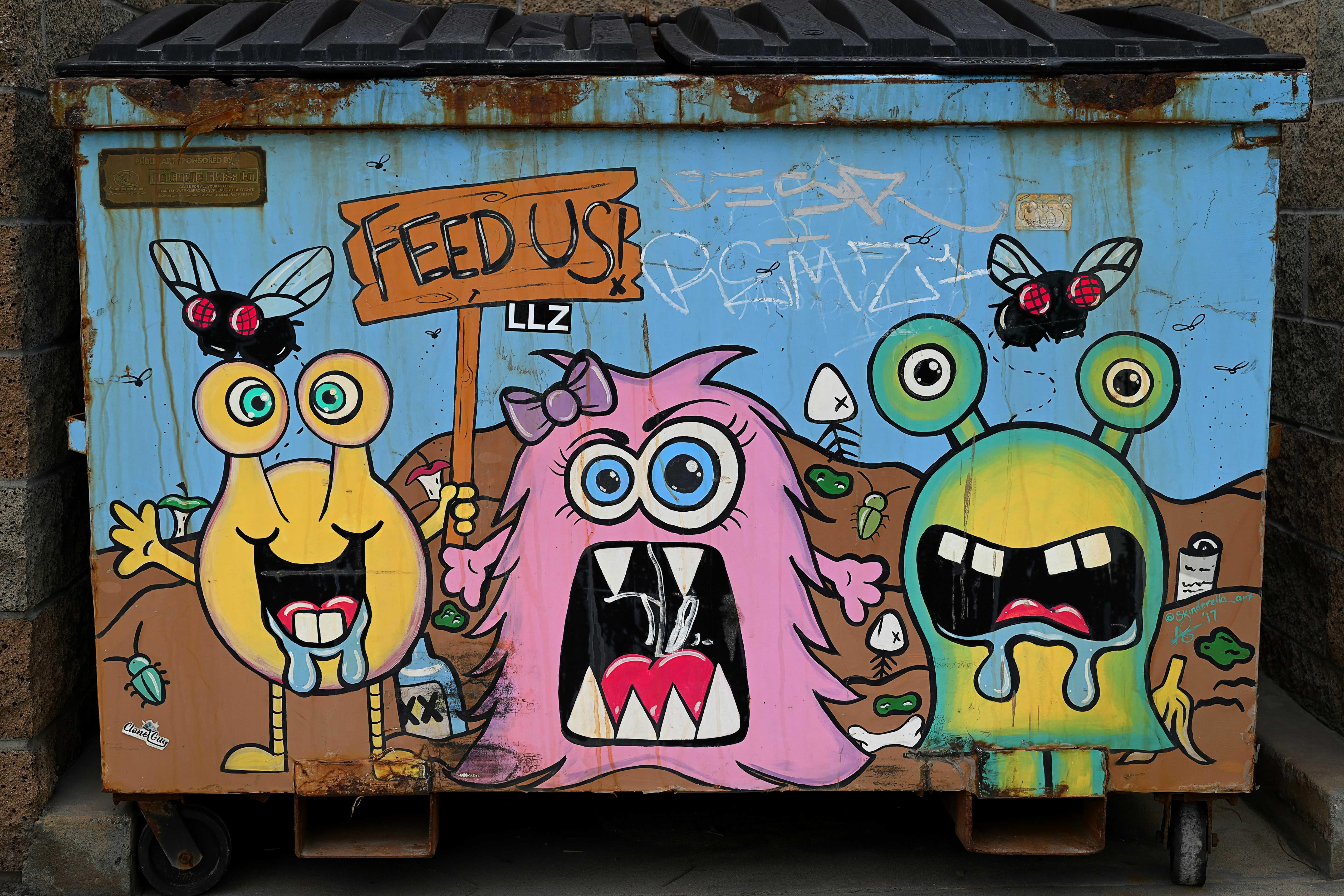 Dumpster with vibrant graffiti art featuring three hungry monsters.