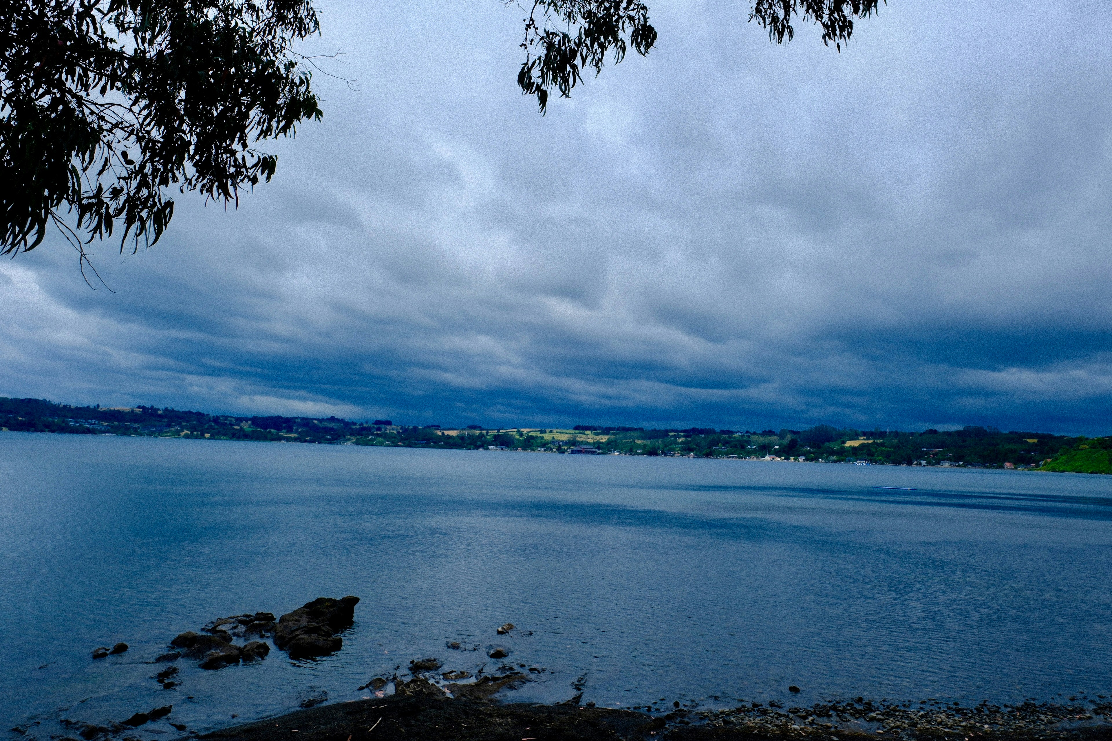 Horizon on a Quiet Lake: Distant Village Under Brooding Skies