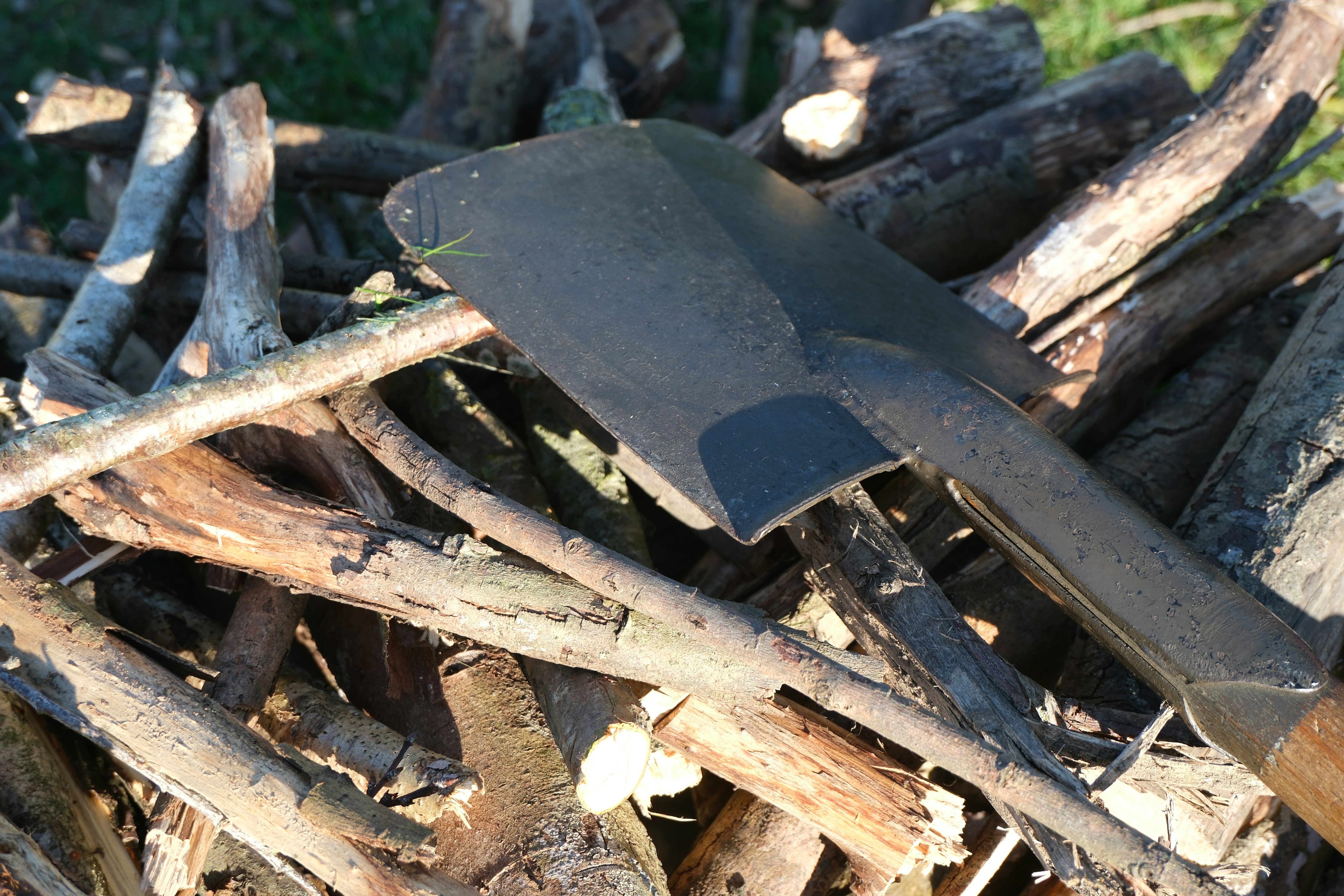 Bent Blade Among Split Wood: a close-up of a machete resting on a pile of sticks