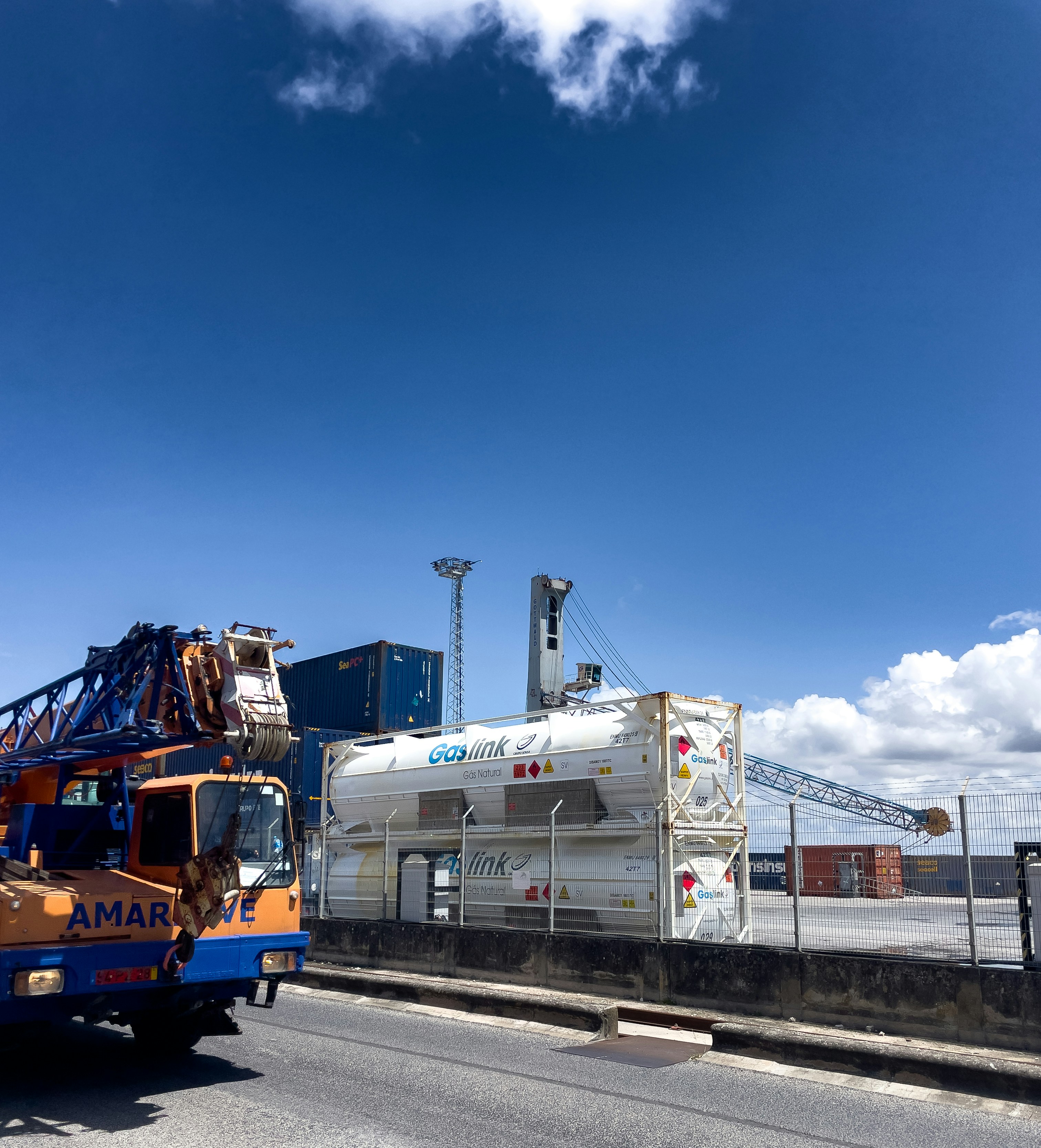 Industrial Harbor: Shipping Tanks and Crane Under a Wide Blue Sky