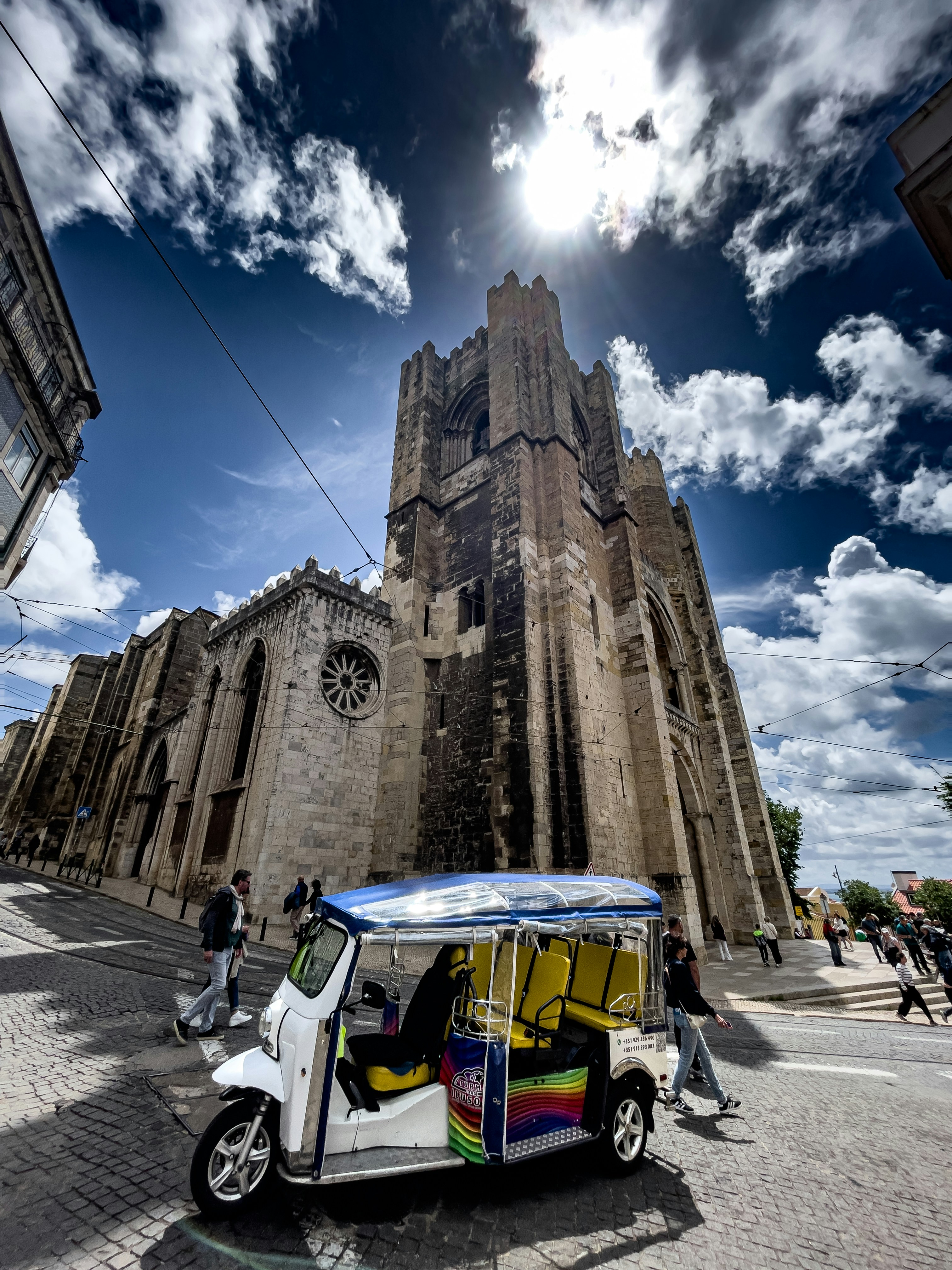 Sunlit Cathedral and Colorful Tuk-Tuk on a Cobblestoned Avenue