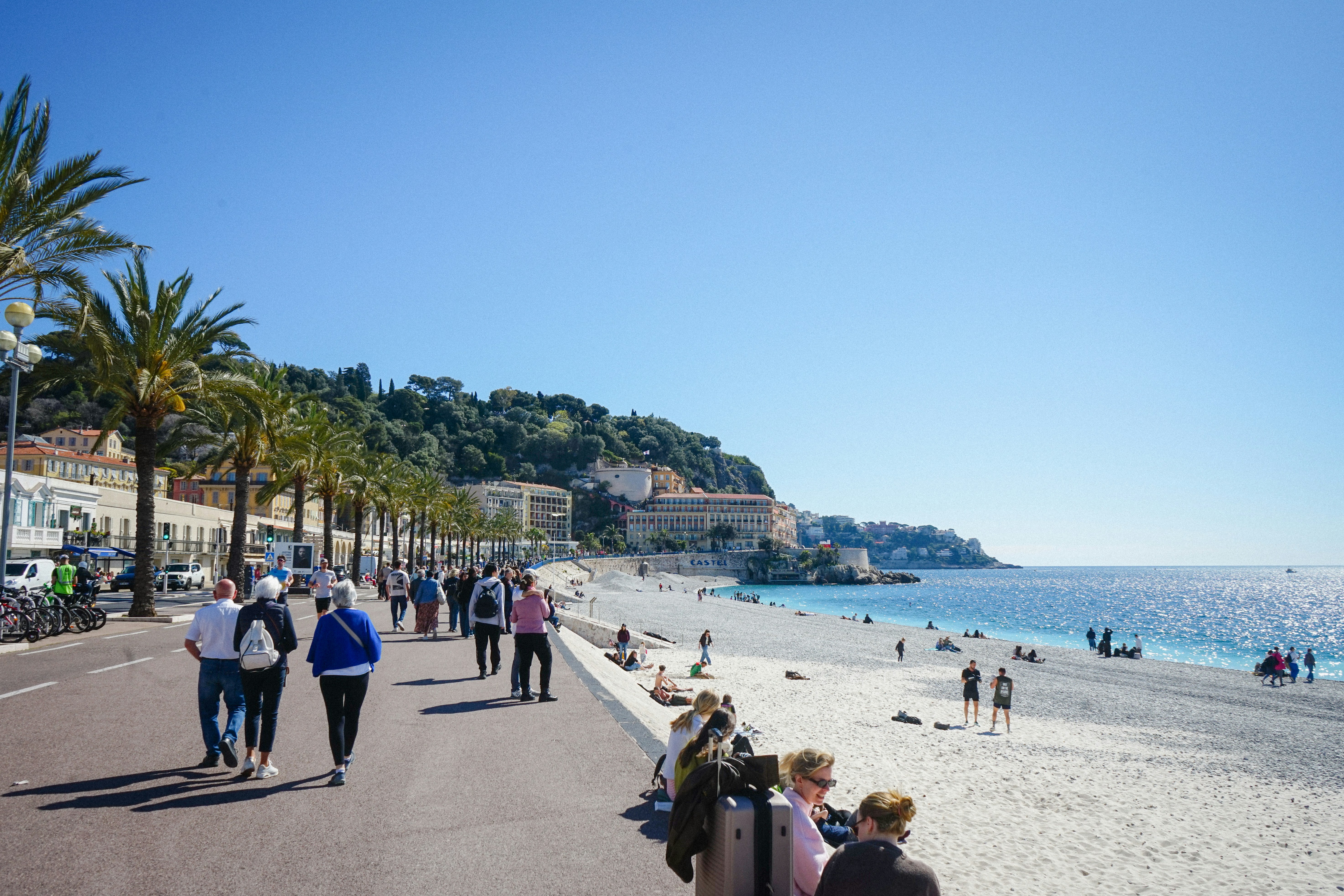 Promenade Pulse: People strolling along a sunlit Côte d’Azur beach