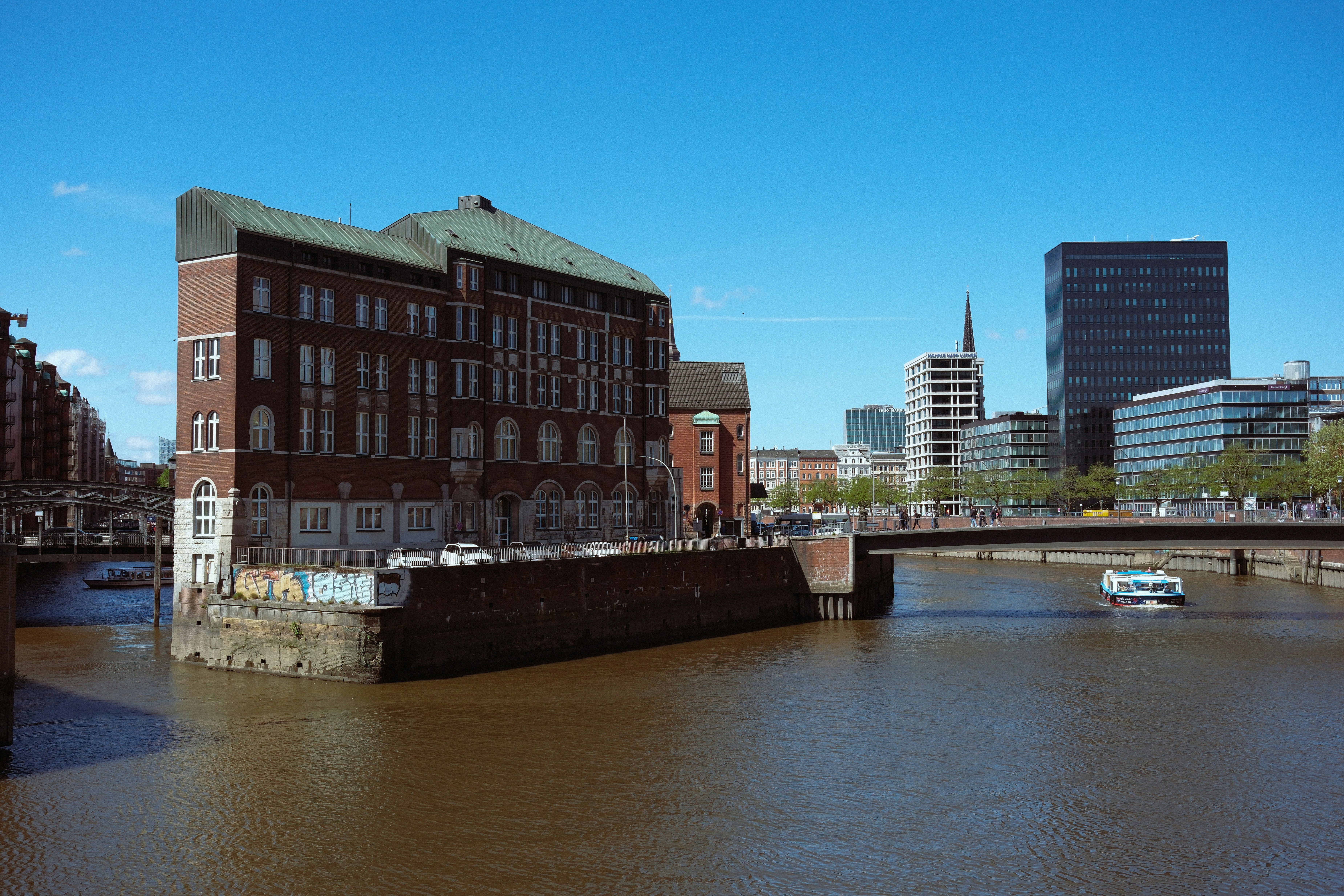 Brick building on a river with modern cityscape background.
