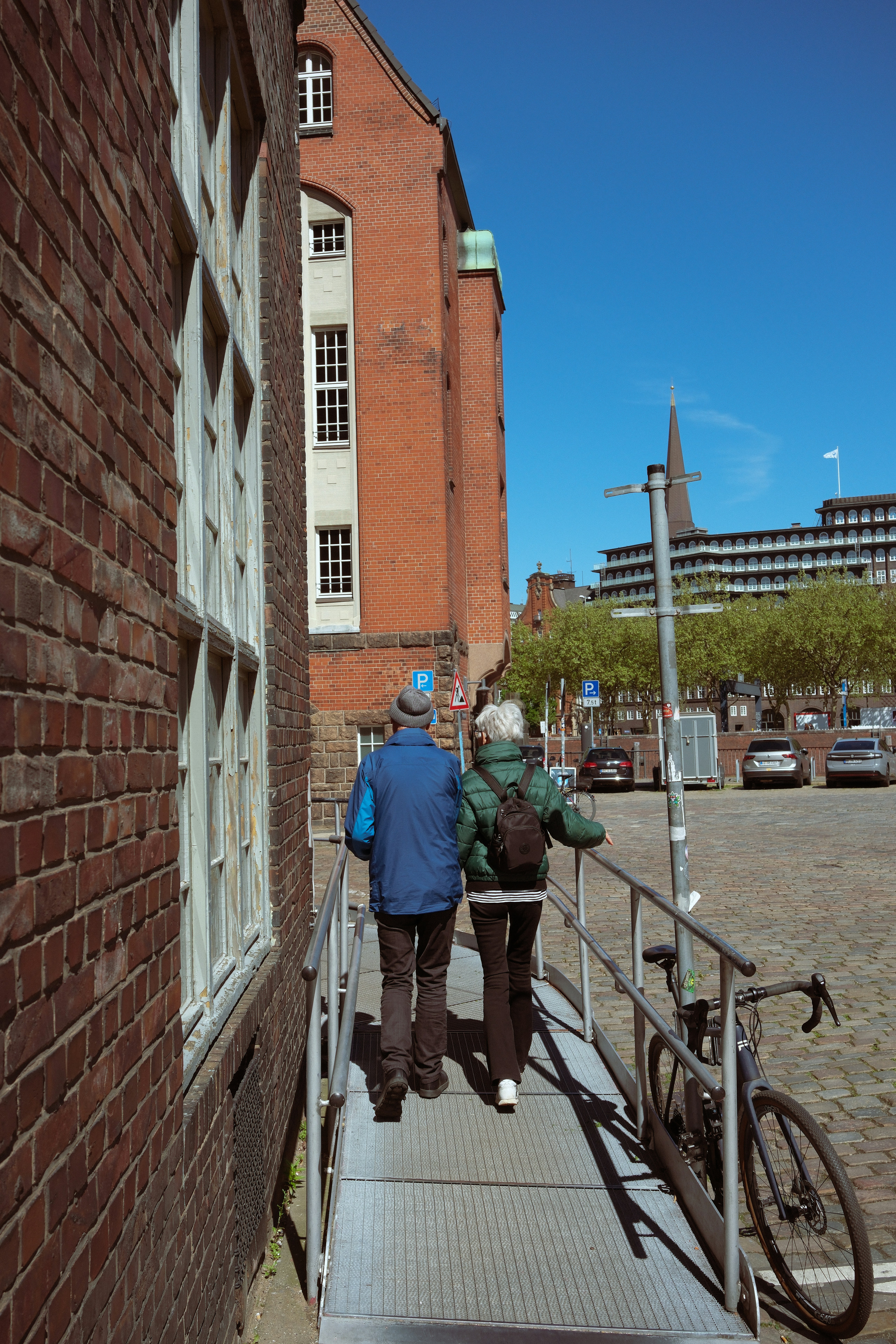 Two Walkers on a Riverside Ramp beside Historic Brick Facades