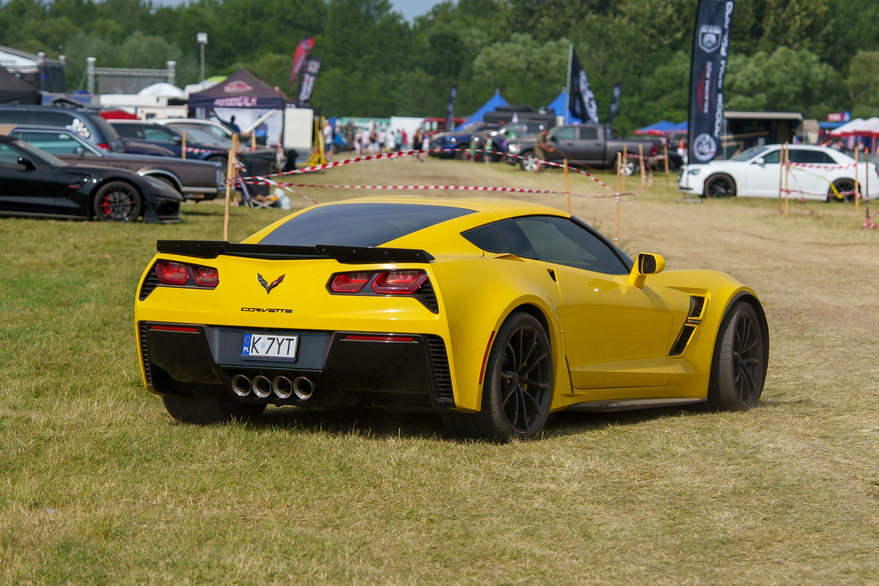 Yellow Corvette at a sunlit car show across a grassy field