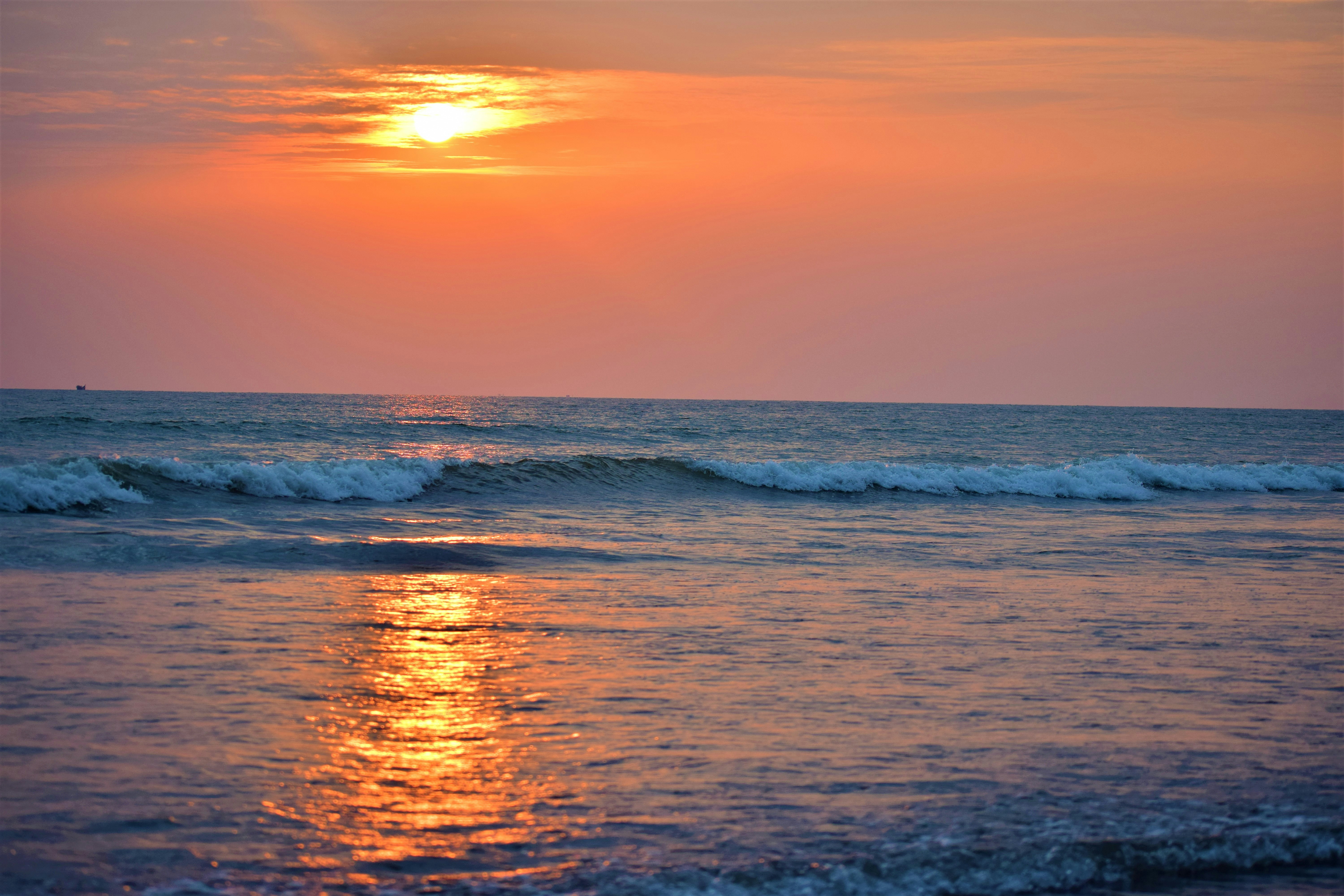 Soft sunset over a calm sea with a glowing orange reflection along the water's surface.