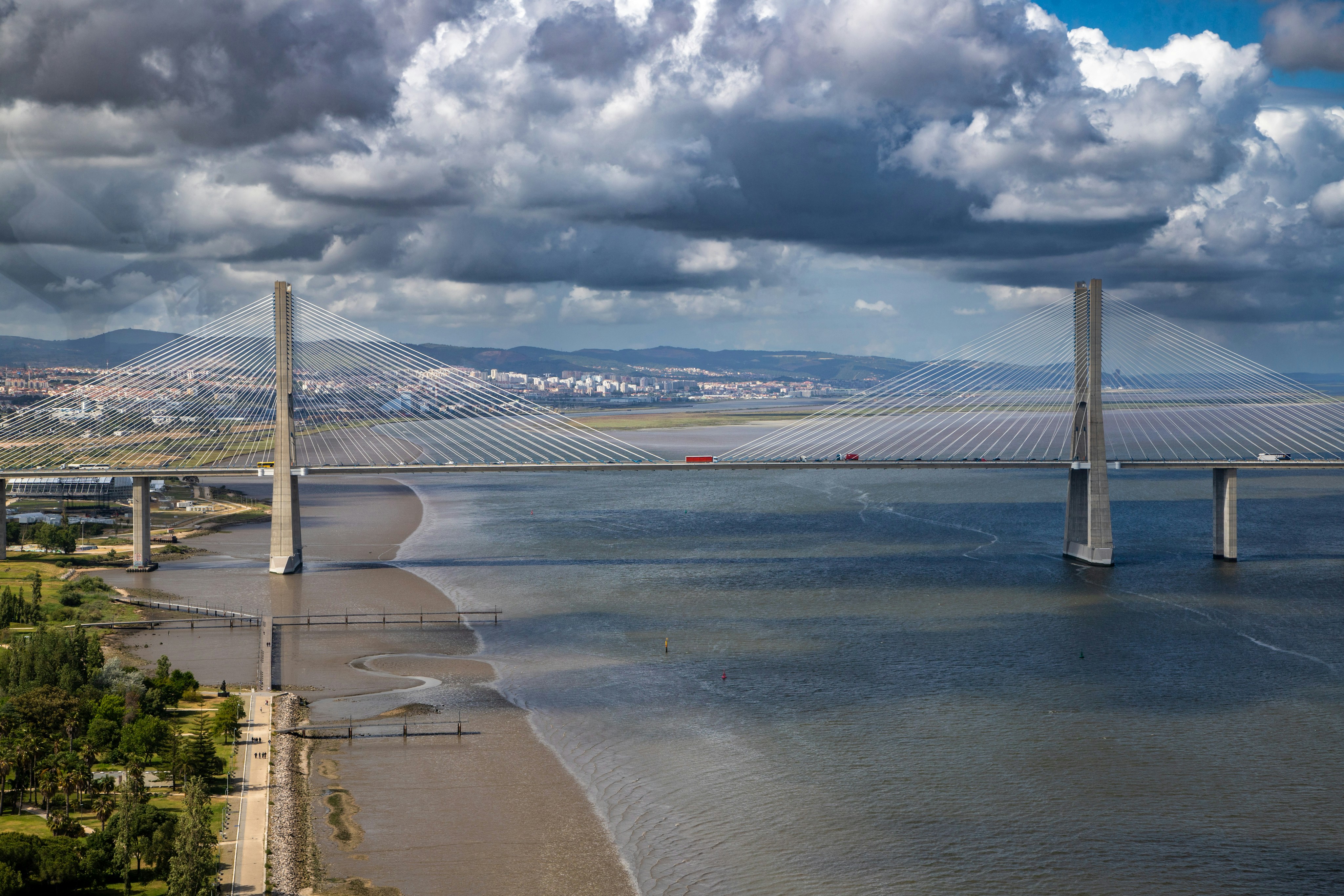 Cable-stretched span over tidal banks under brooding clouds