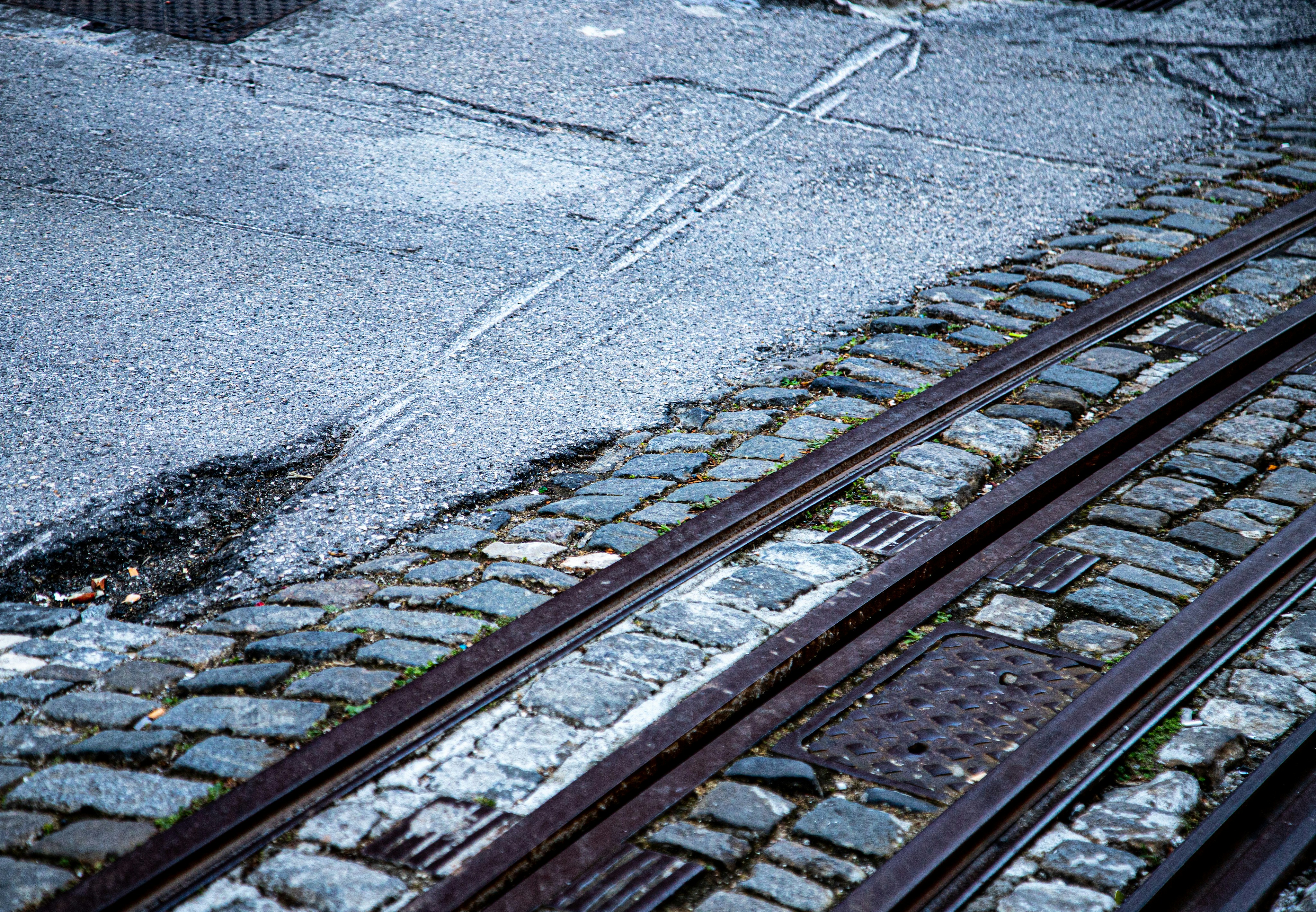 Rusted Rails at the Edge of Wet Cobbled Street