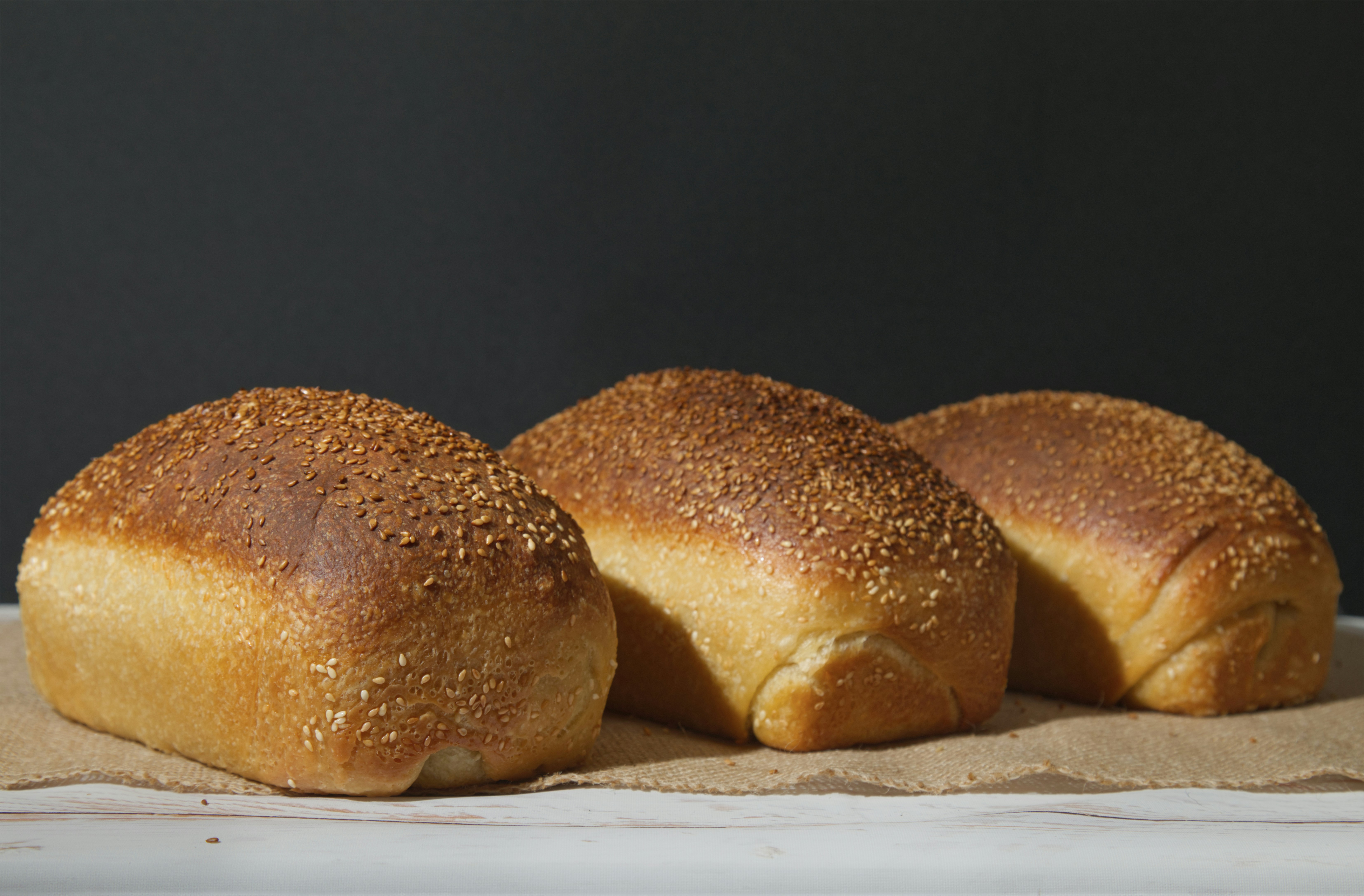 Three sesame-topped buns resting on a linen underlit by a soft studio glow