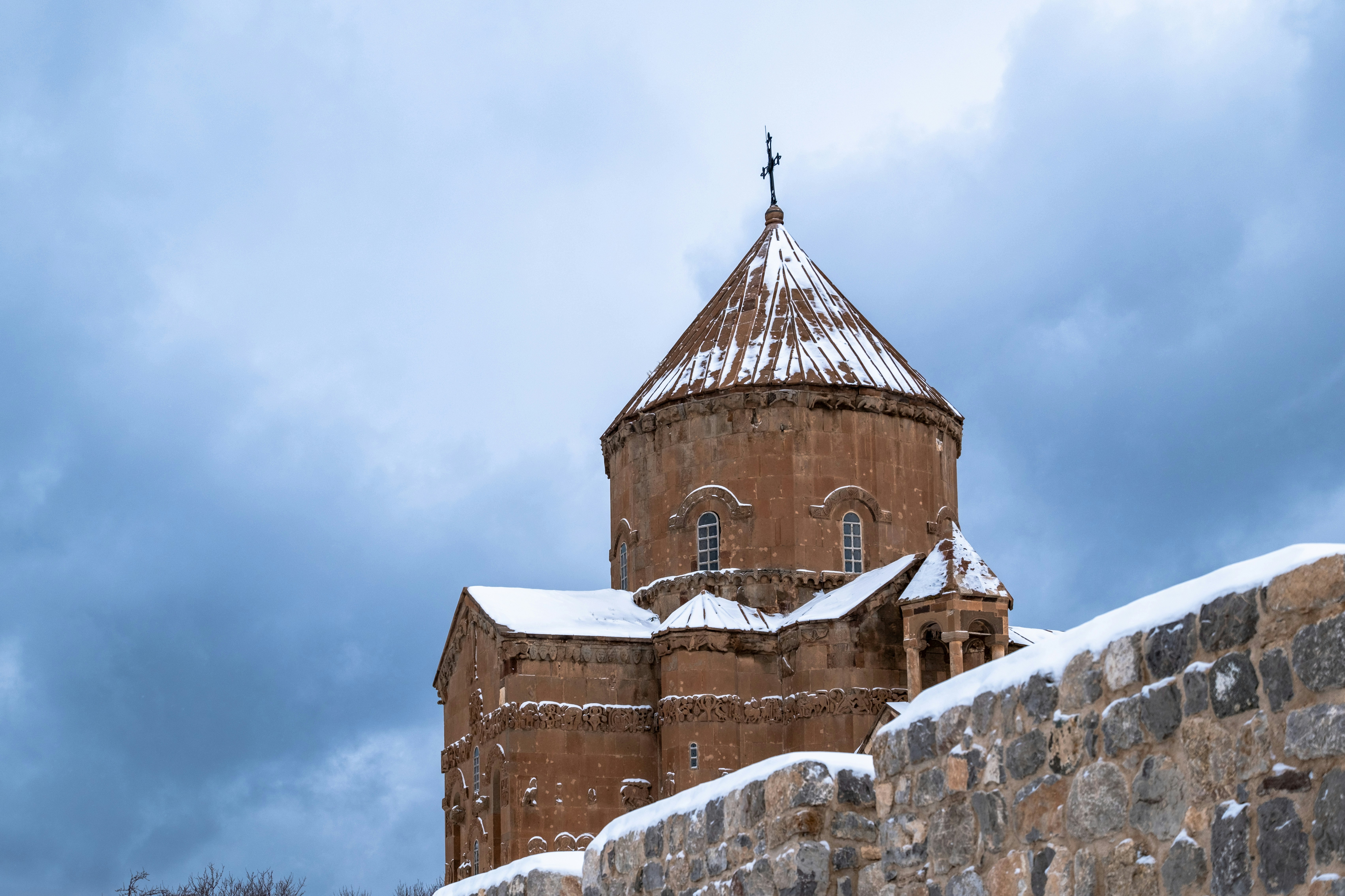 Snow-kissed fortress tower rises over a stone wall under a moody sky