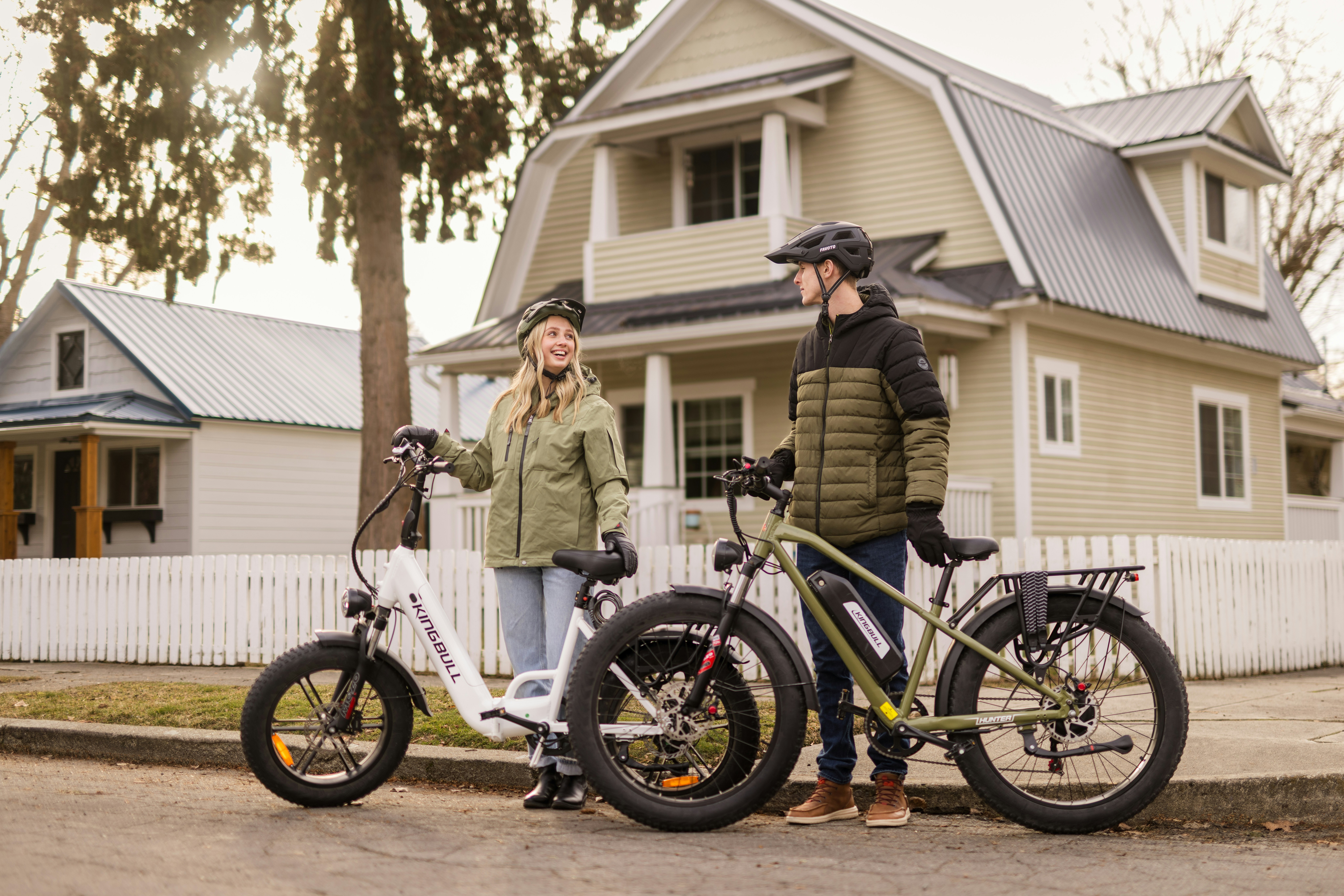 Two cyclists pause with e-bikes in a quiet suburban street